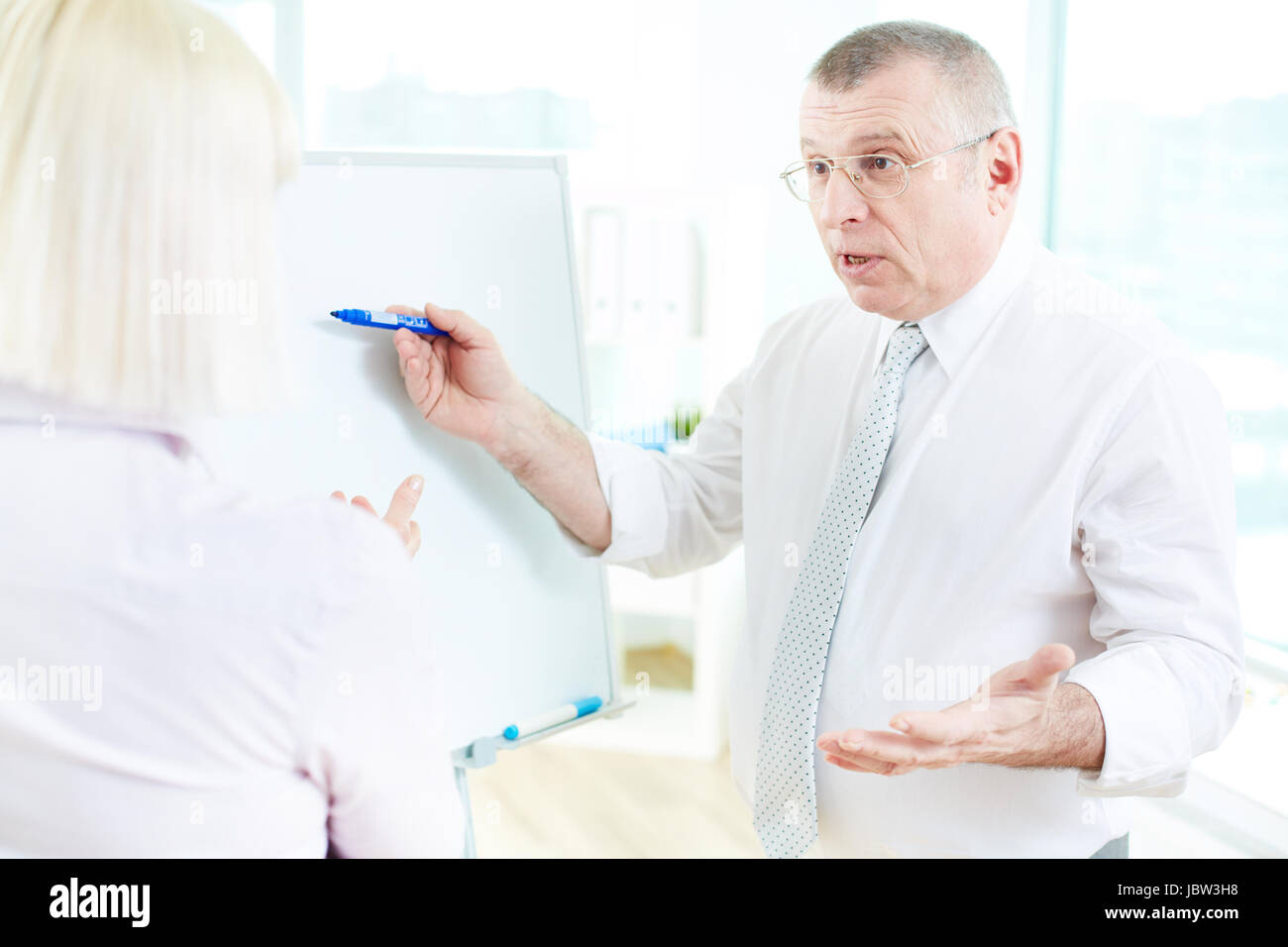 Image of mature businessman teaching his partner on whiteboard at ...