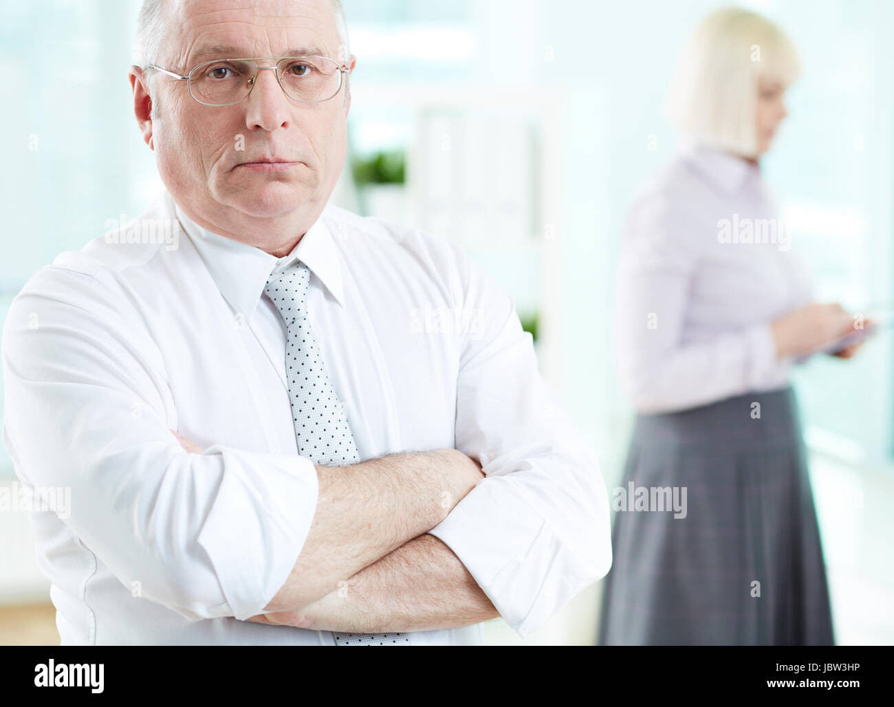 Portrait of serious boss looking at camera with female standing on ...
