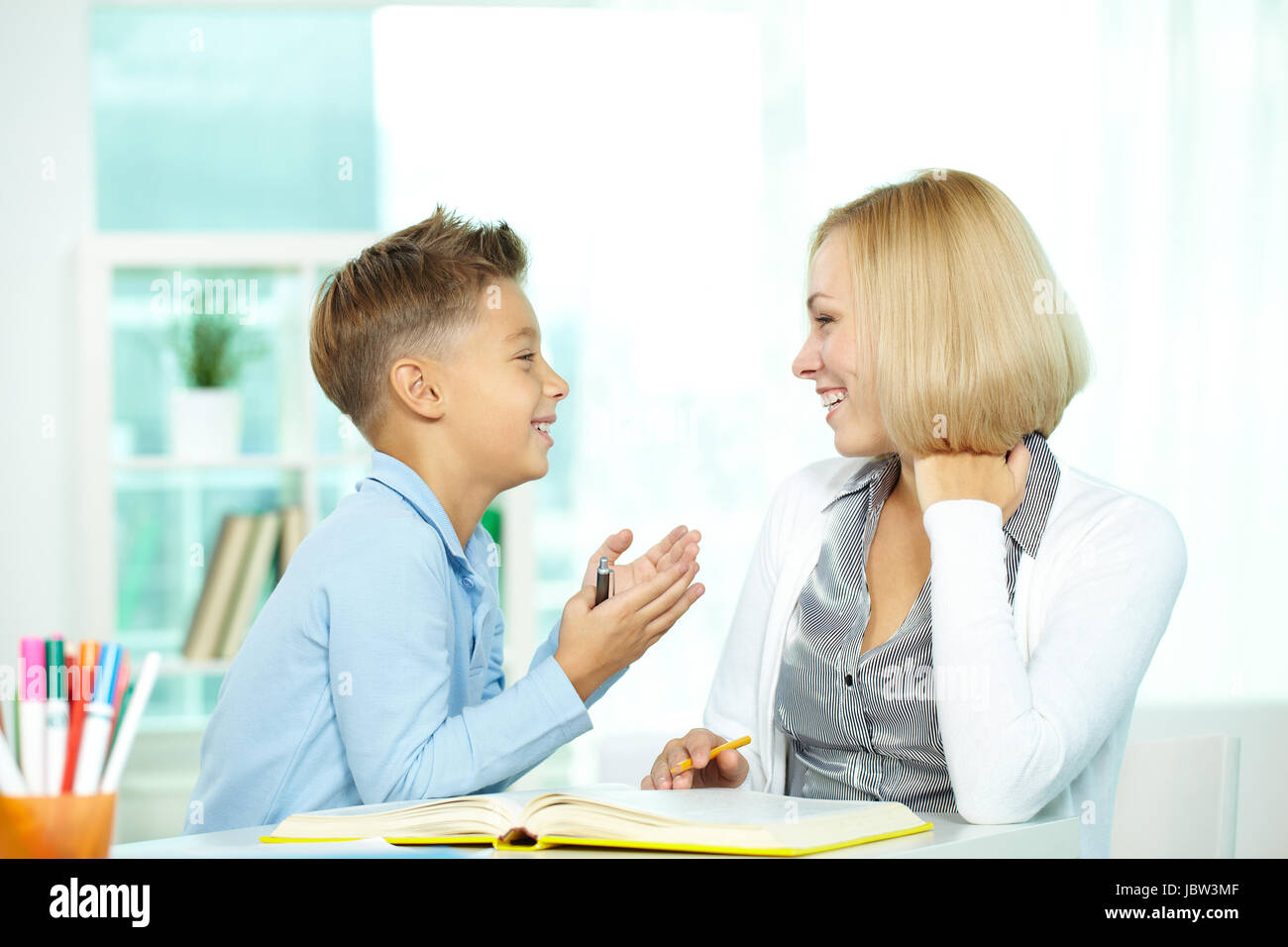Portrait of pretty tutor and diligent pupil looking at each other while ...
