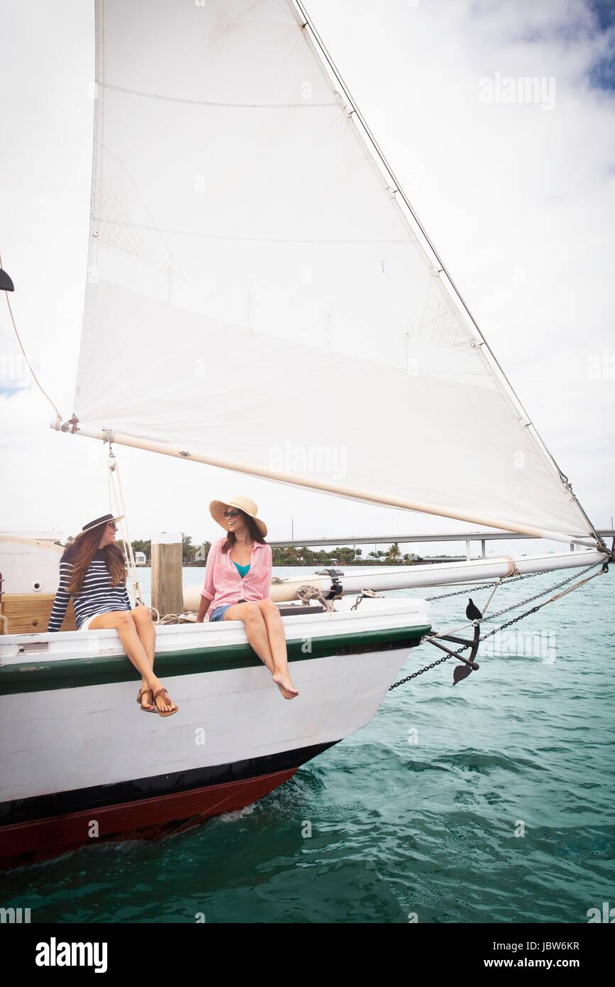 Two women on sitting on edge of sailing boat, legs dangling over the ...