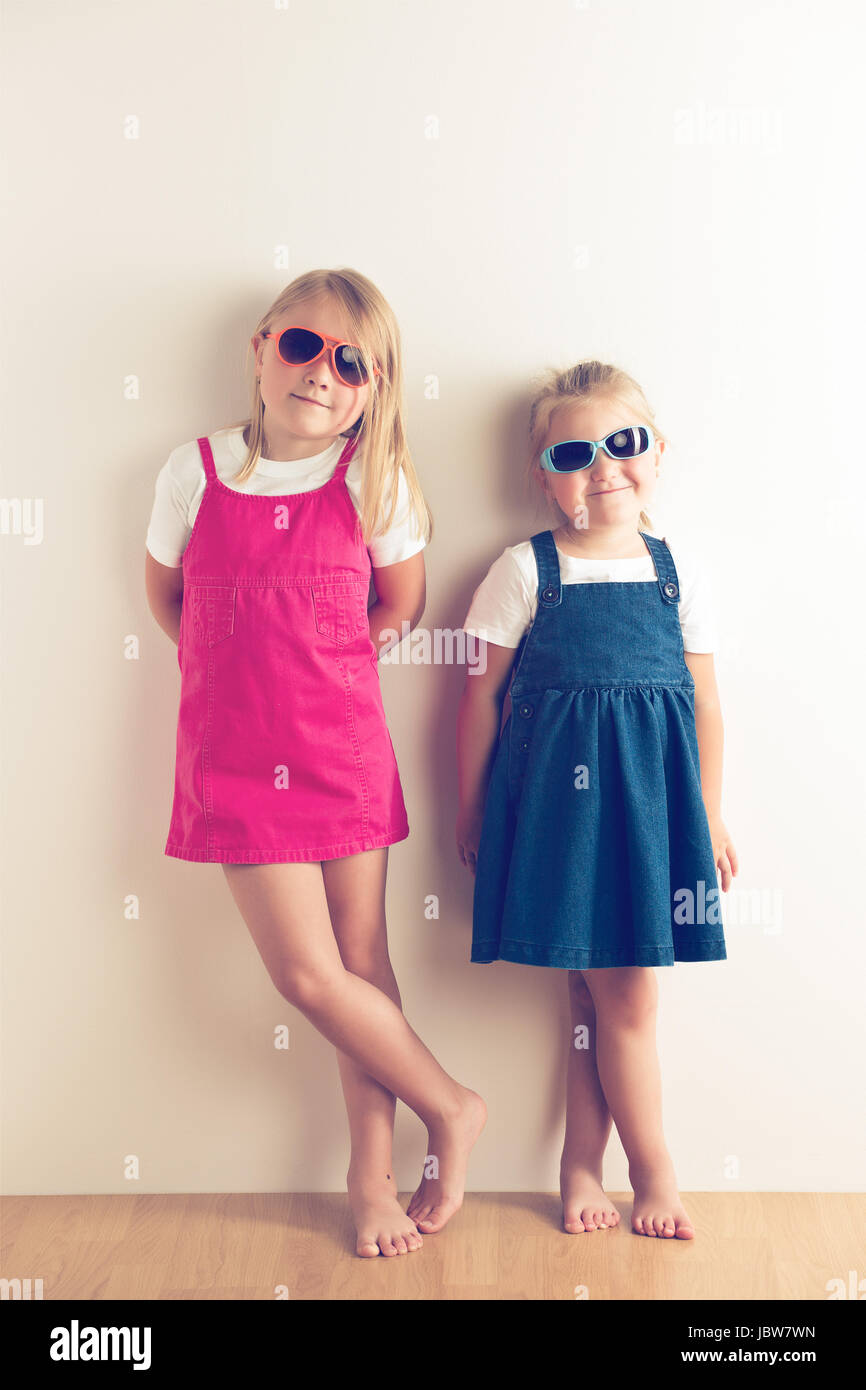 Two little girls posing in front of a walll. Studio shot Stock Photo ...