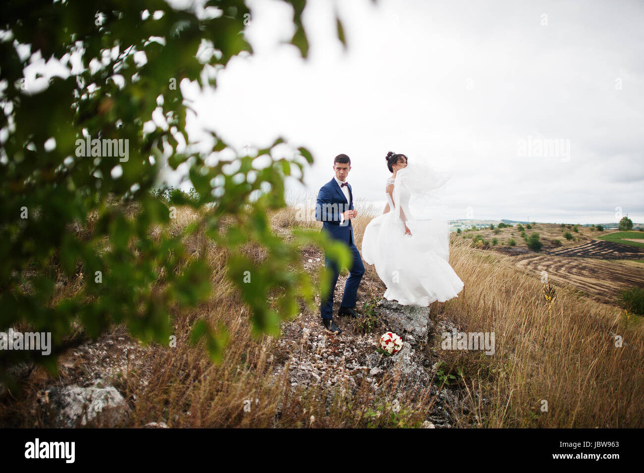 Gorgeous wedding couple standing on the stone on a windy wedding day in ...