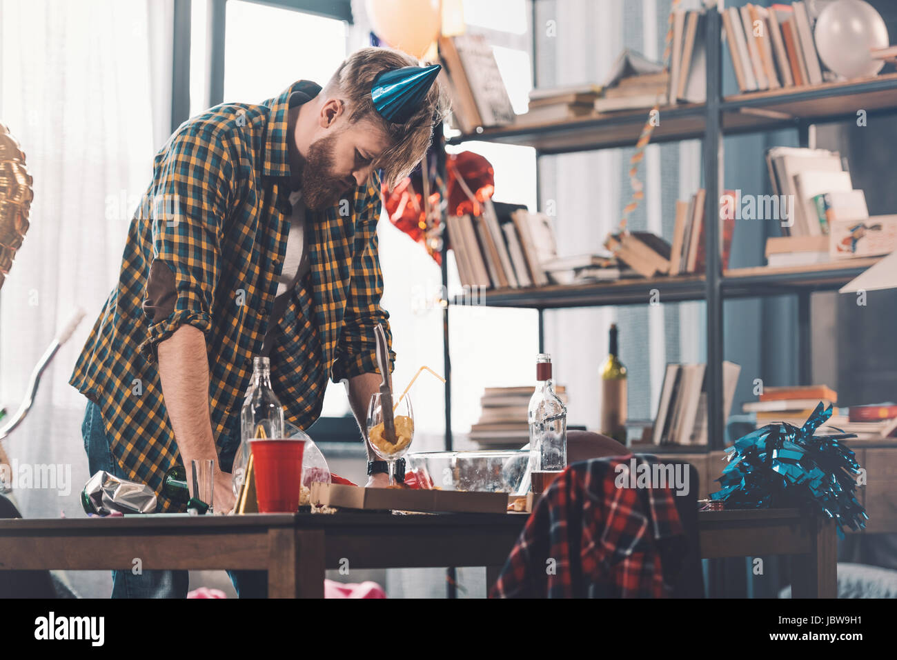 man with hangover cleaning messy room after party Stock Photo - Alamy