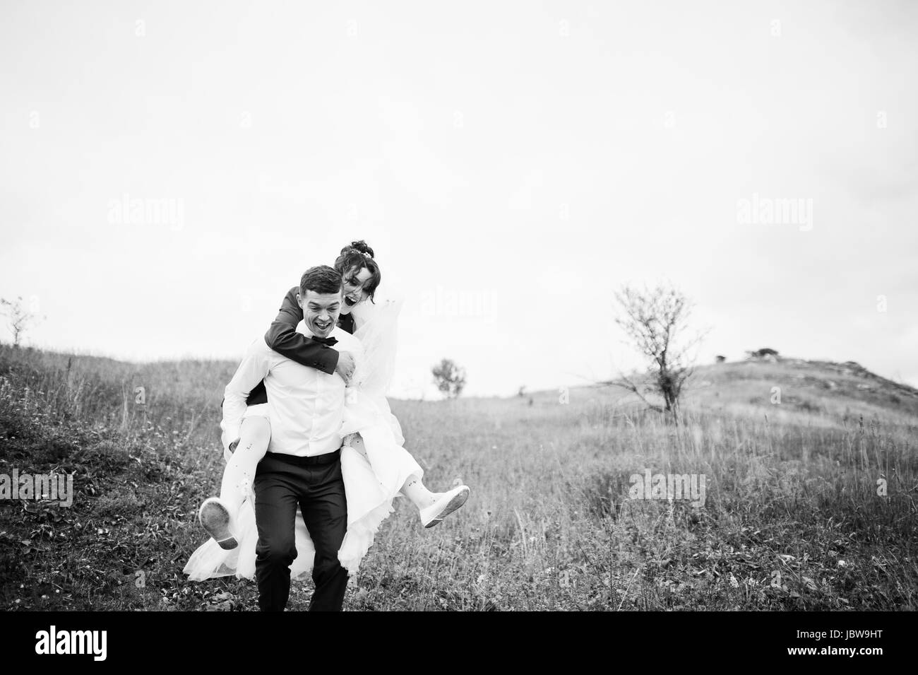 Happy bride riding her husband's back on their wedding day on the of ...
