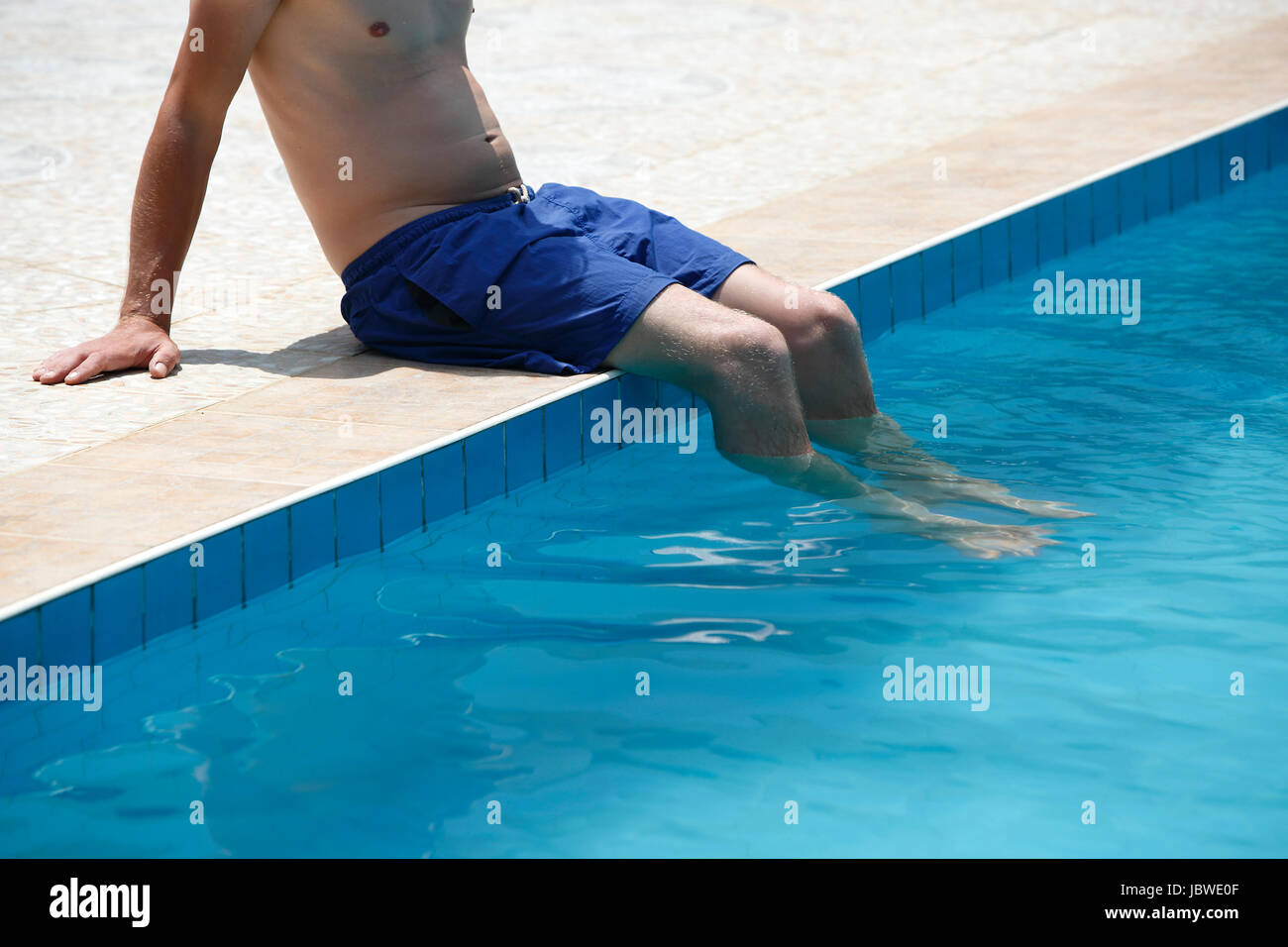 Attractive man with blue swimsuit sitting on the edge of the swimming ...