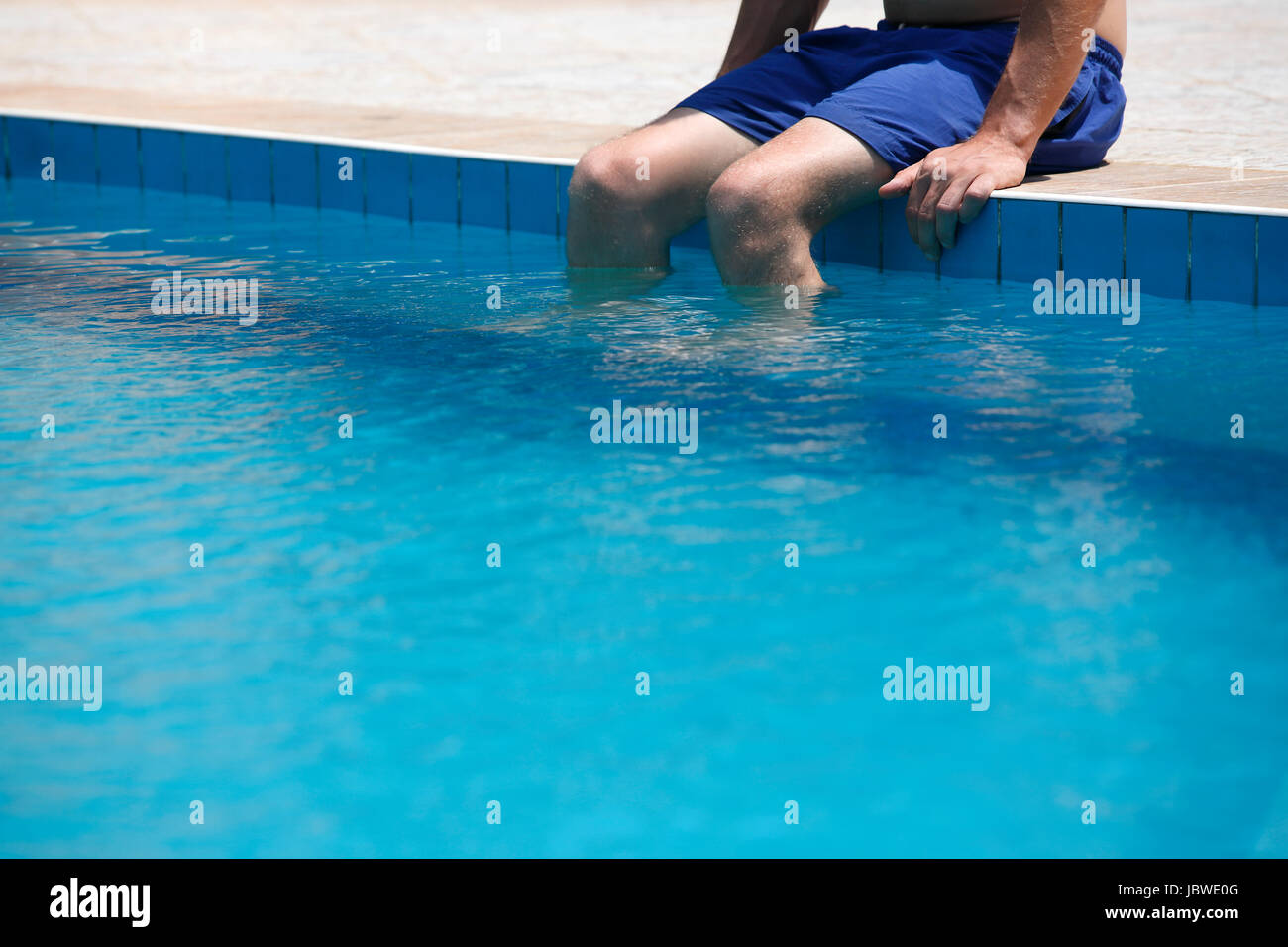 Attractive man with blue swimsuit sitting on the edge of the swimming ...