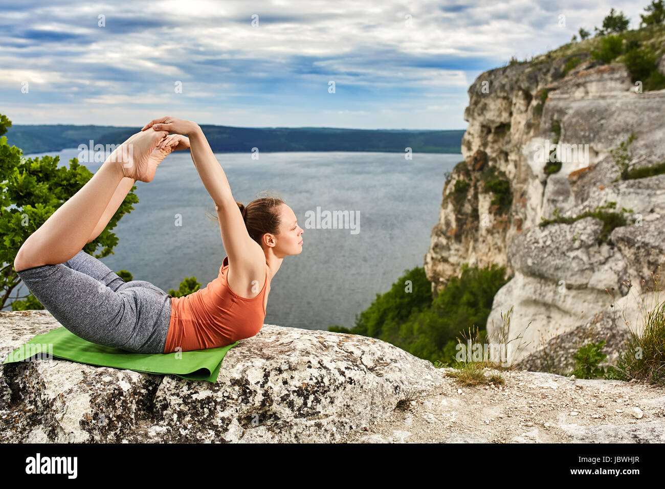 Young woman makes yoga pose on the rock above beautiful big river ...