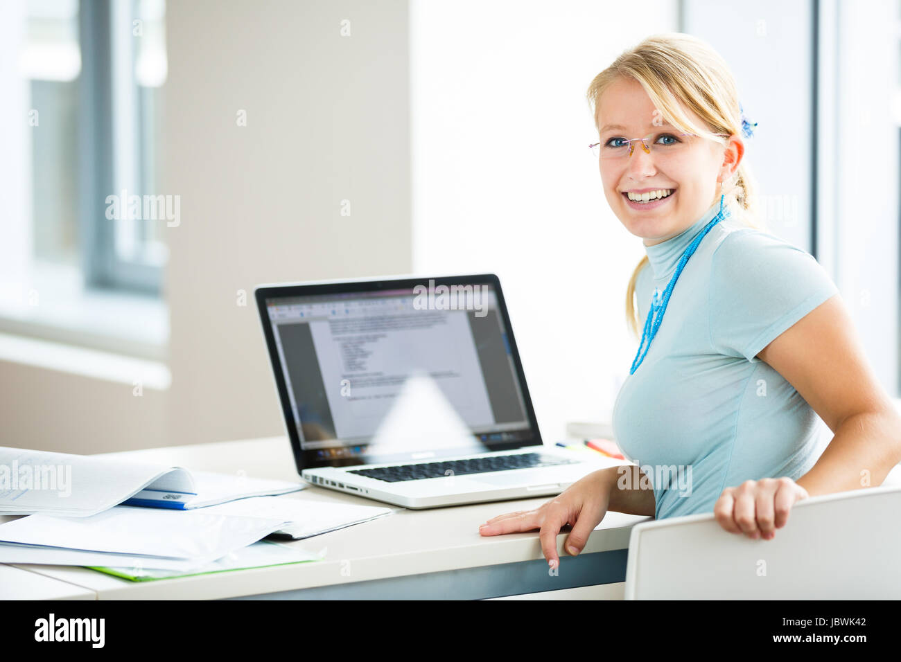 In the library - pretty, female student with books, papers and laptop ...