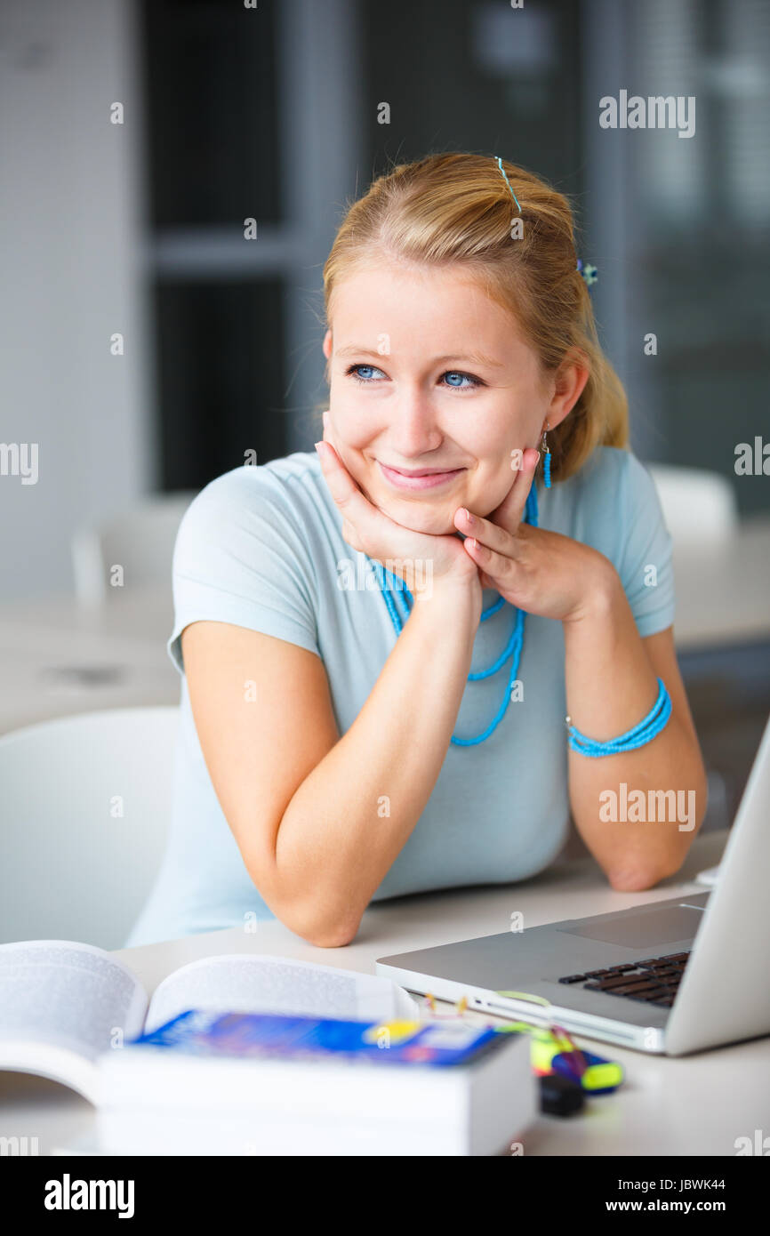 In the library - pretty, female student with books, papers and laptop ...