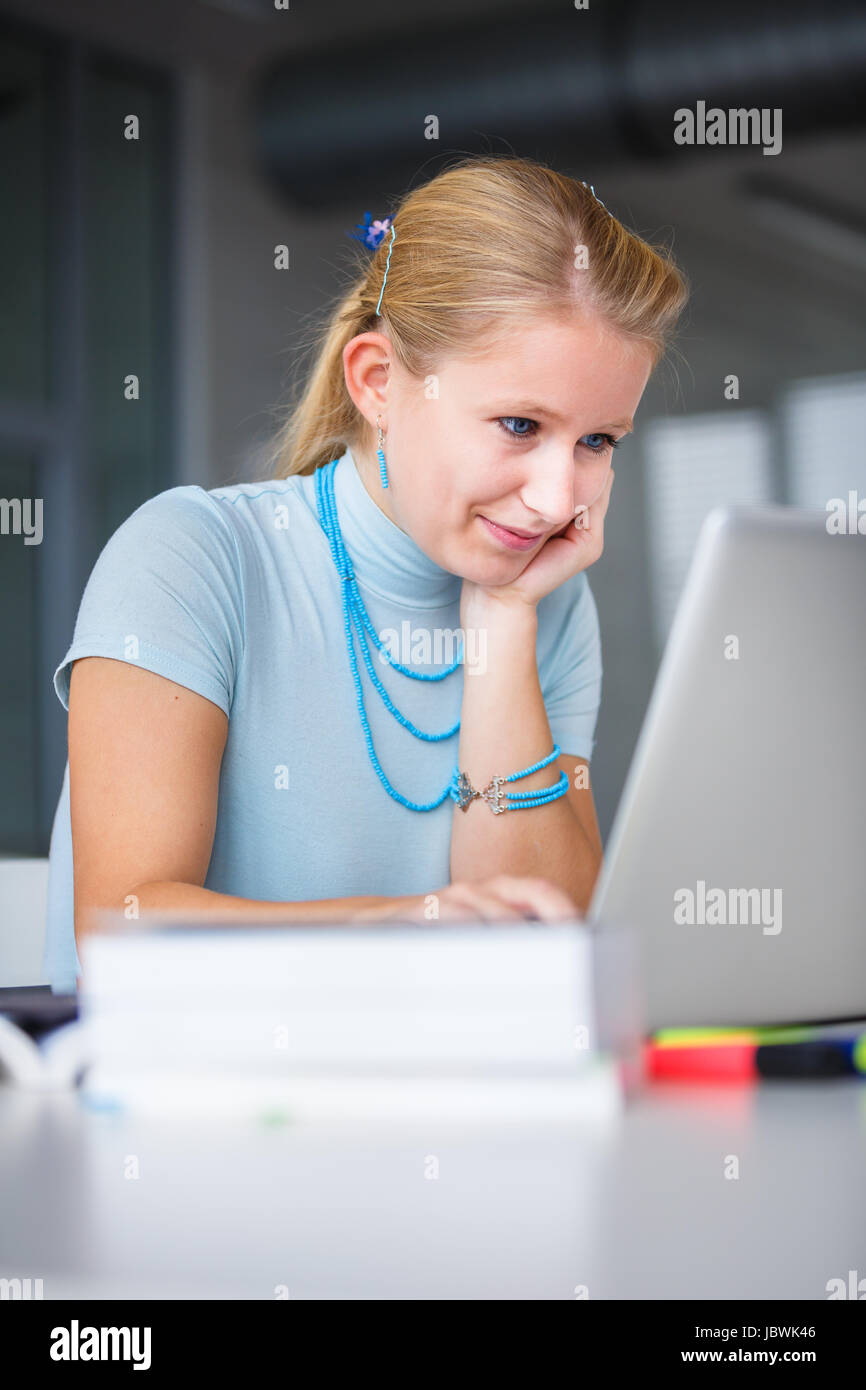 In the library - pretty, female student with books, papers and laptop ...