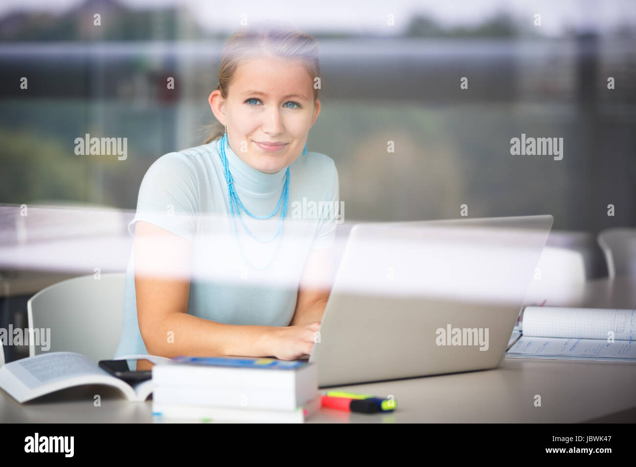 In the library - pretty, female student with books, papers and laptop ...