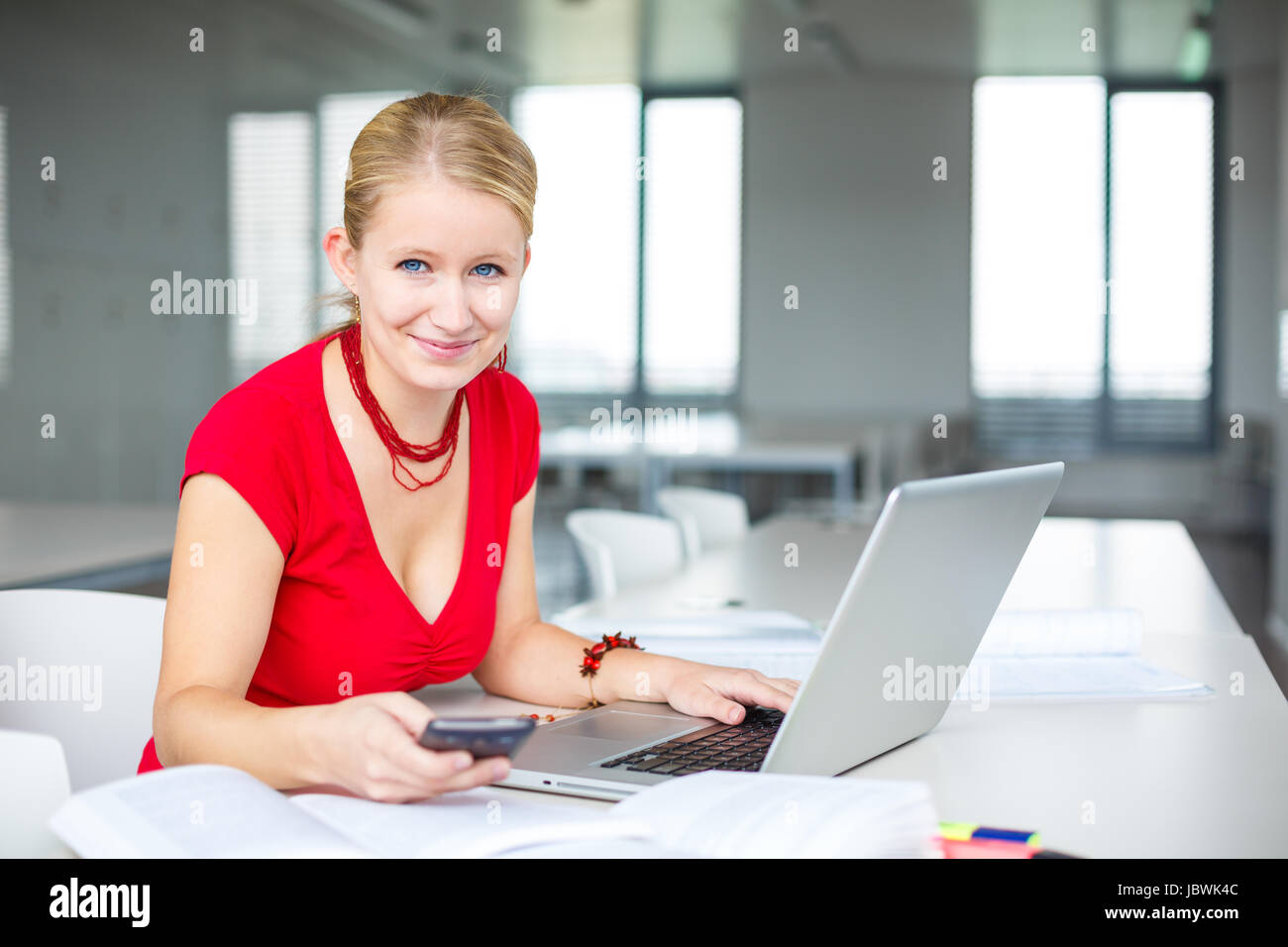 In the library - pretty, female student with books, papers and laptop ...