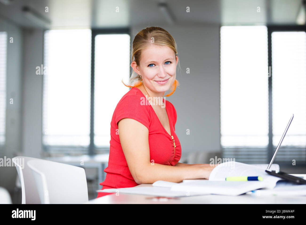 In the library - pretty, female student with books, papers and laptop ...