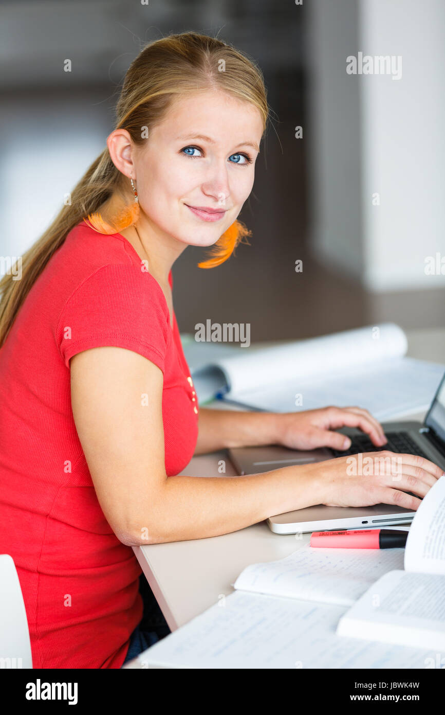 In the library - pretty, female student with books, papers and laptop ...