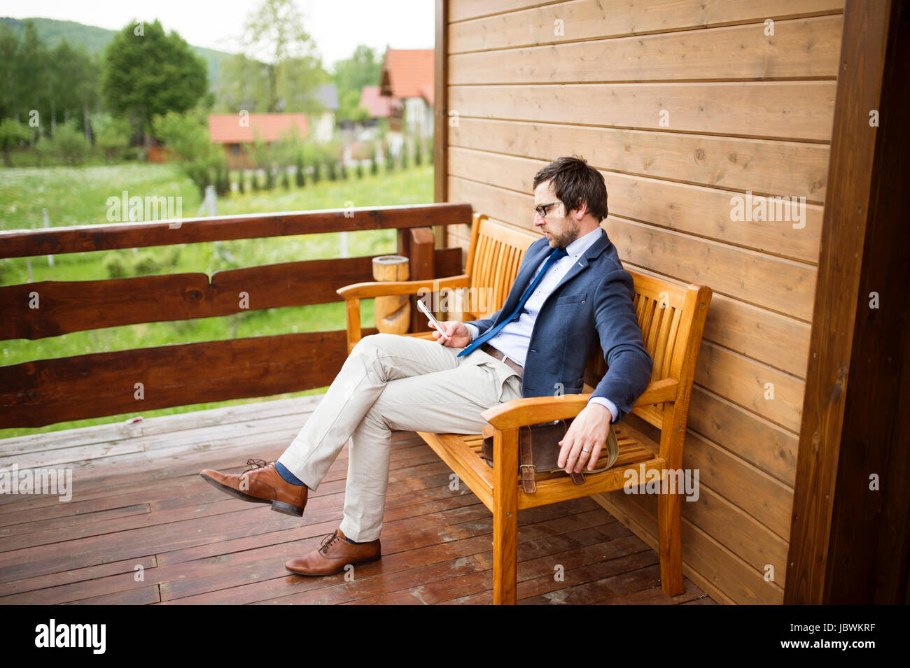 Businessman with smart phone sitting on front porch Stock Photo - Alamy