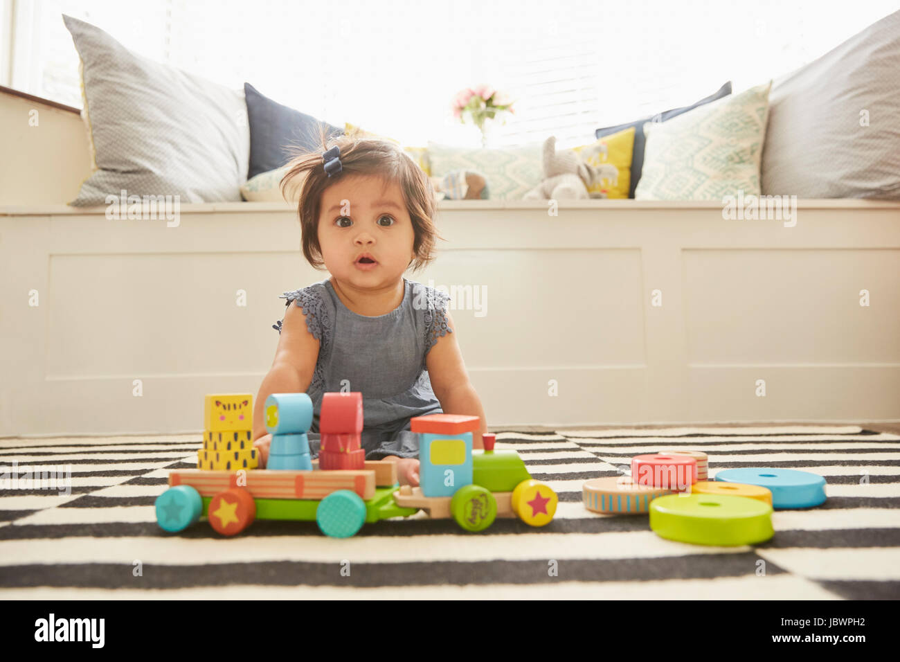 Portrait of baby girl sitting on rug playing with toy train Stock Photo ...