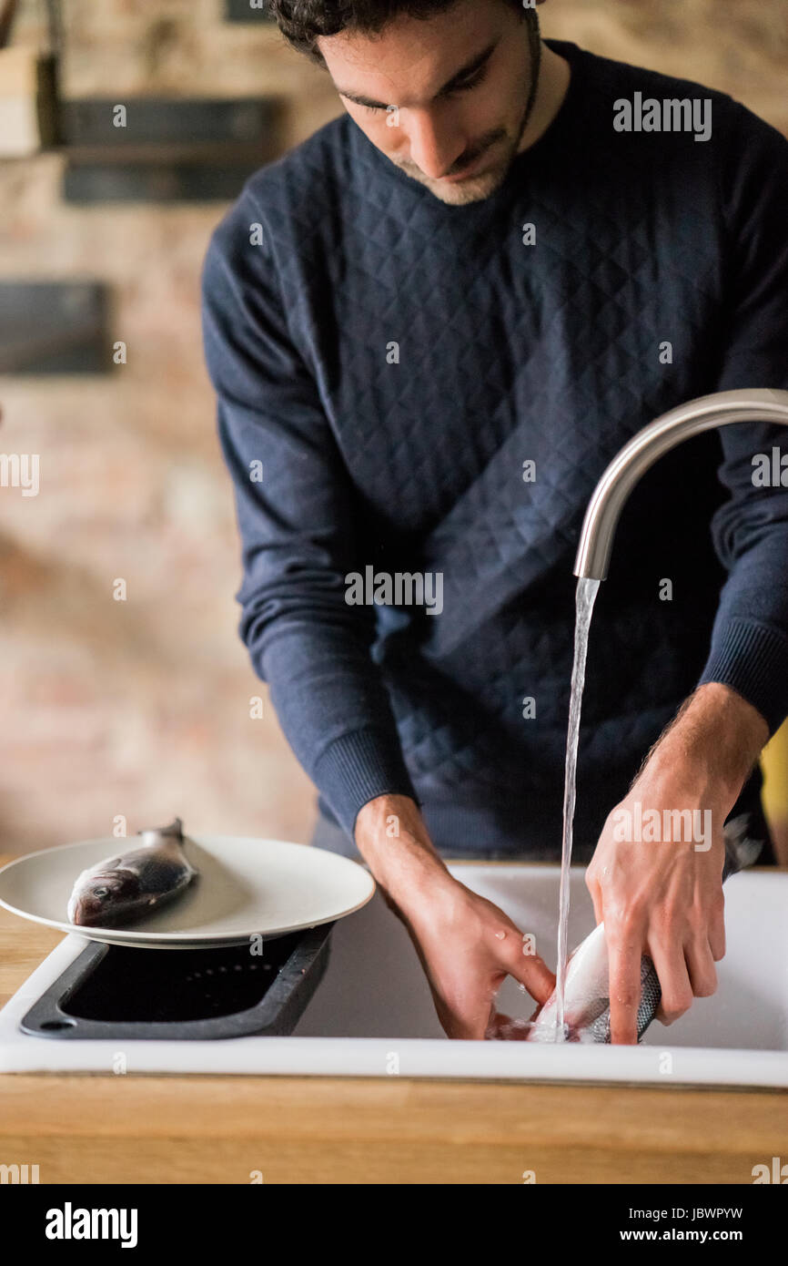 Young man washing fish at kitchen sink Stock Photo - Alamy