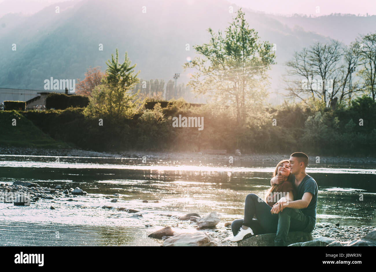Romantic couple sitting on rocks beside river, smiling Stock Photo - Alamy