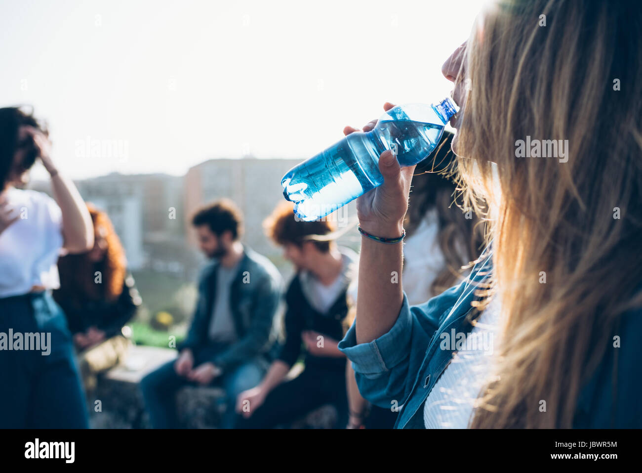 Group of friends enjoying roof party, young woman drinking from water ...
