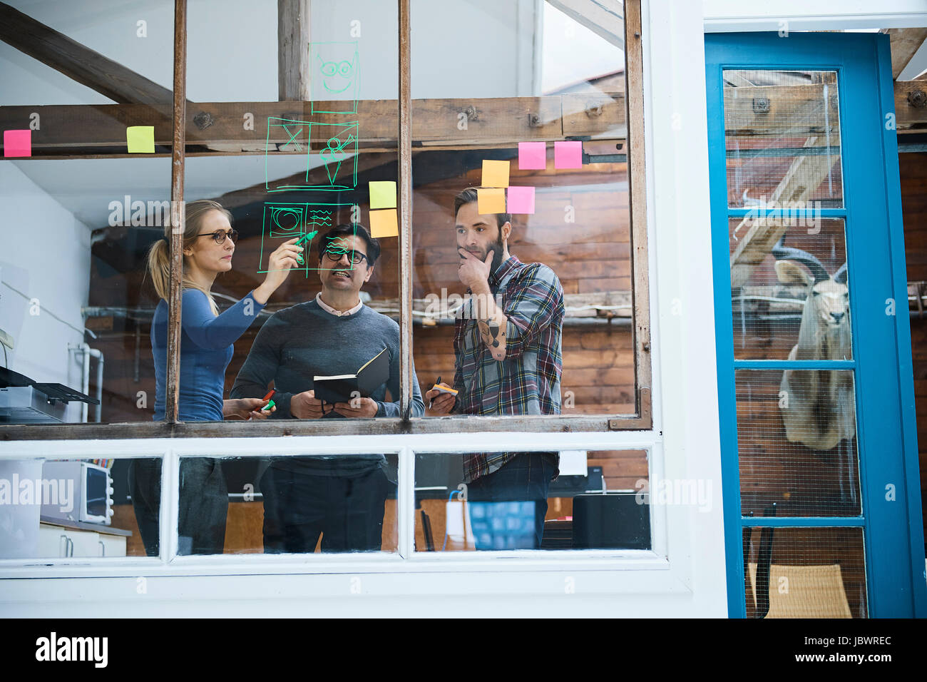 Design team writing on adhesive notes and drawing on design studio ...