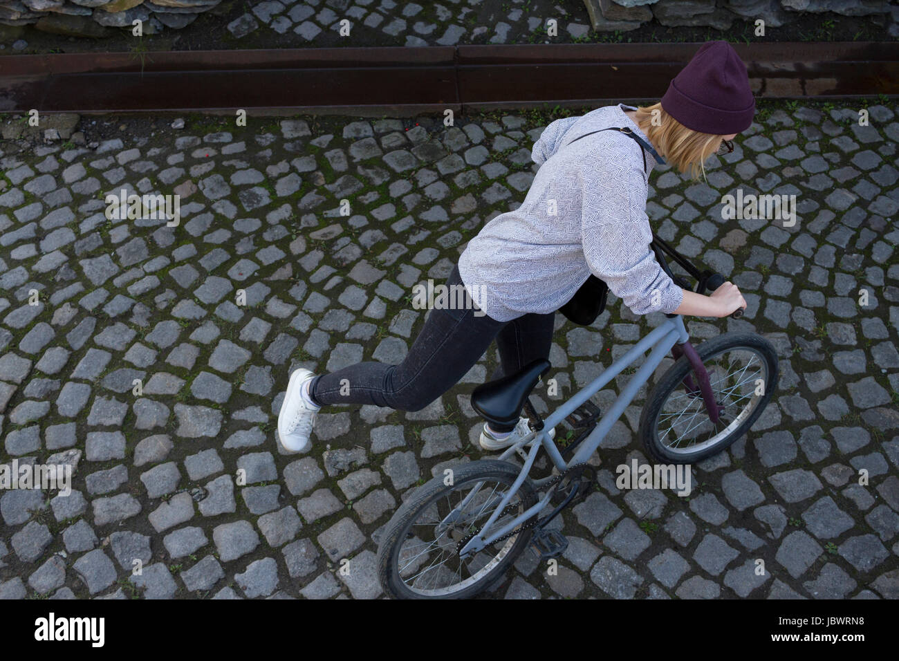 Overhead view of young woman mounting BMX bicycle in cobbled street ...