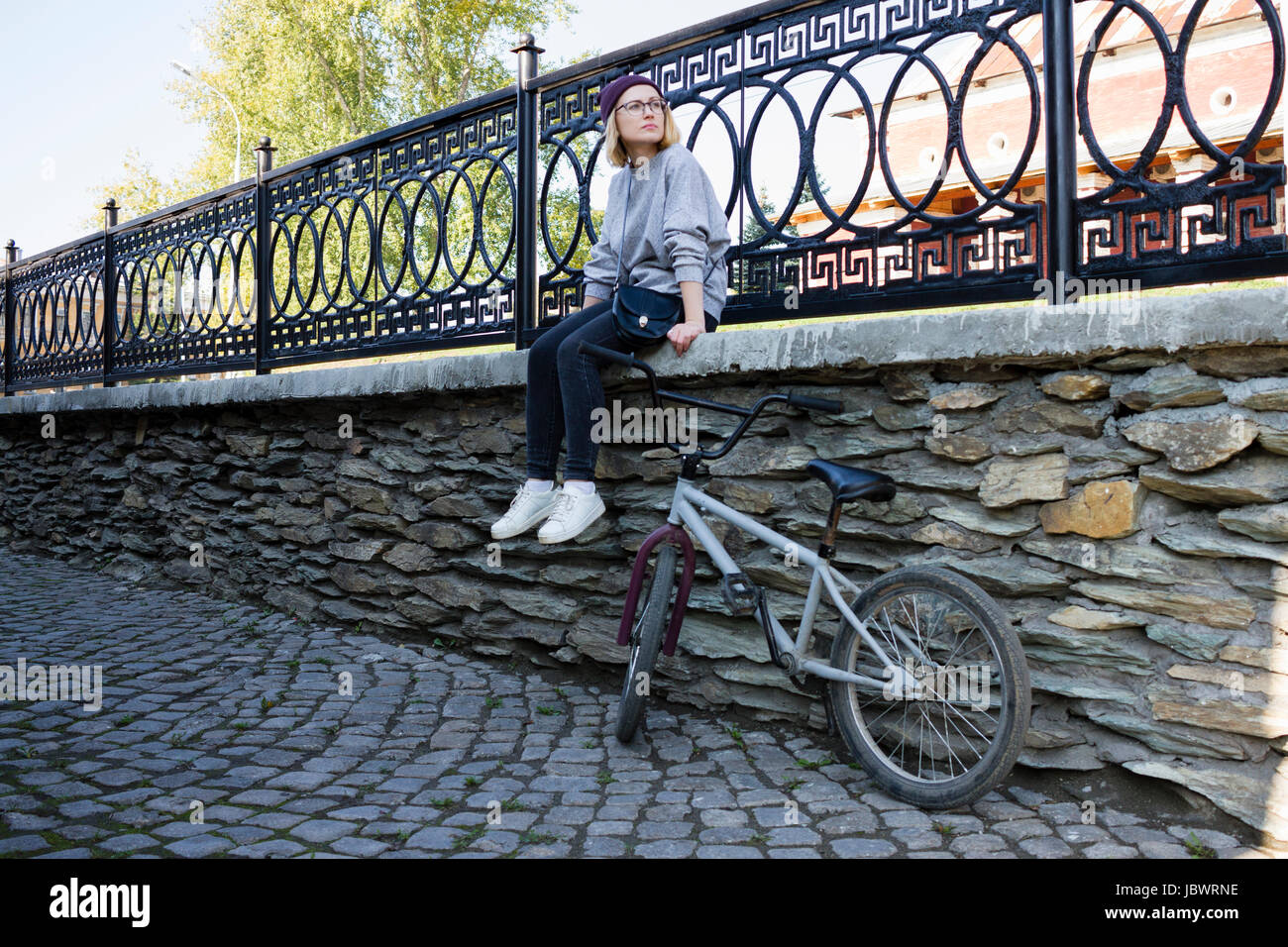 Young female BMX cyclist looking over her shoulder from wall on cobbled ...