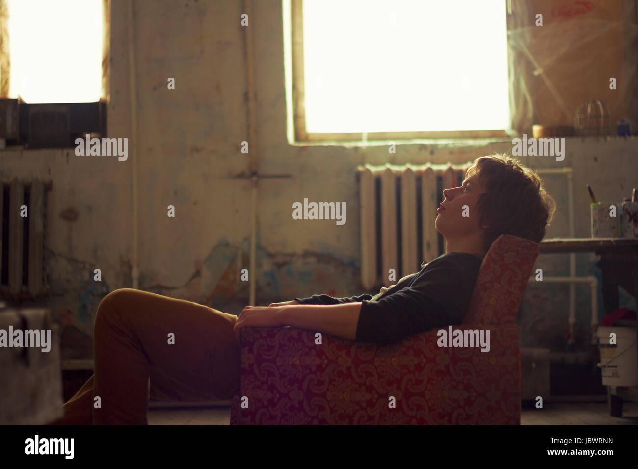 Young man sitting on vintage armchair in artist studio gazing upward ...