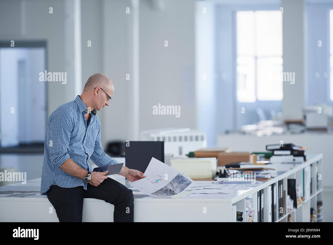 Man in open plan office looking at blueprint Stock Photo - Alamy
