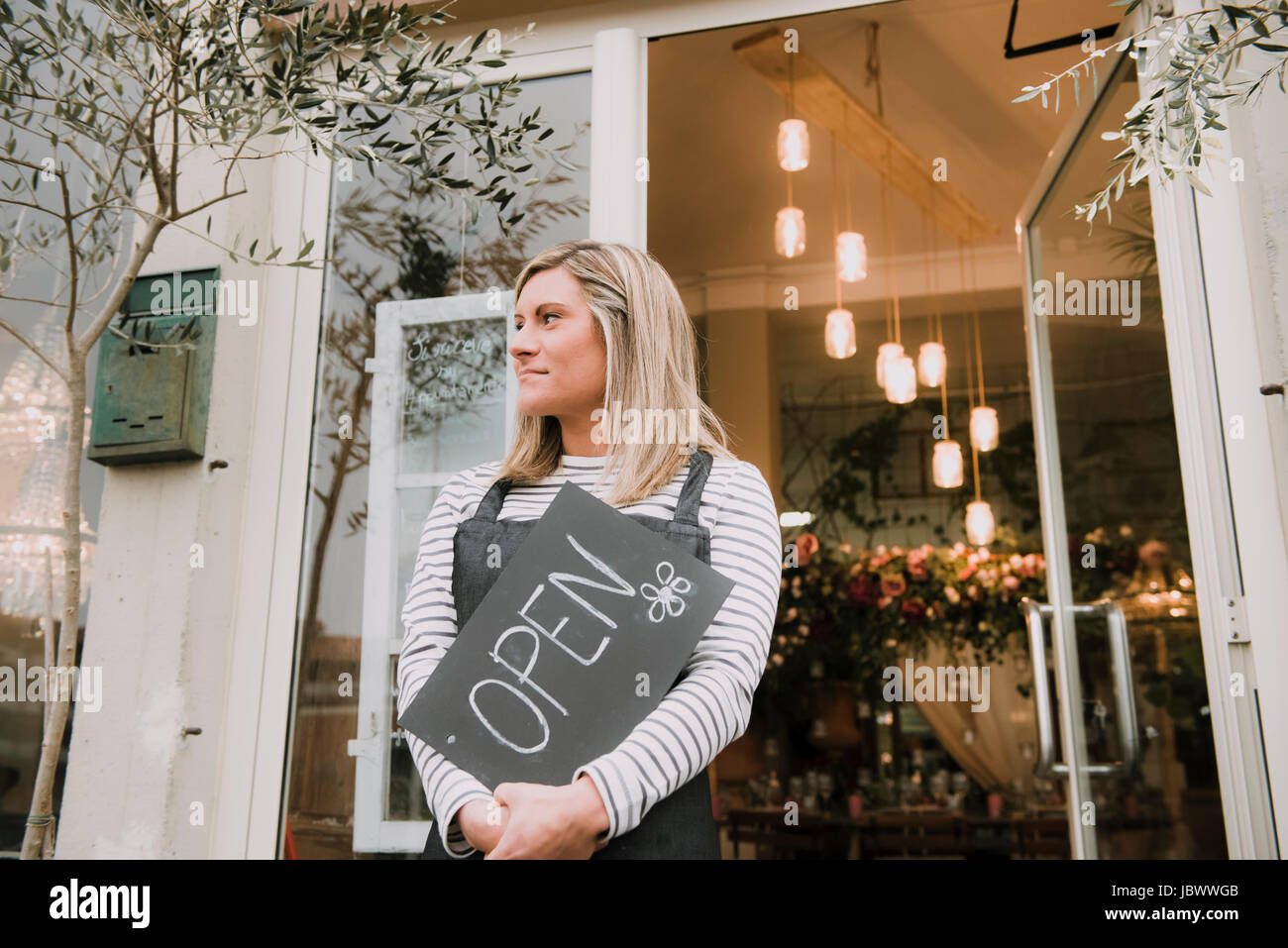 Florist standing outside flower shop, holding 'open' sign Stock Photo ...