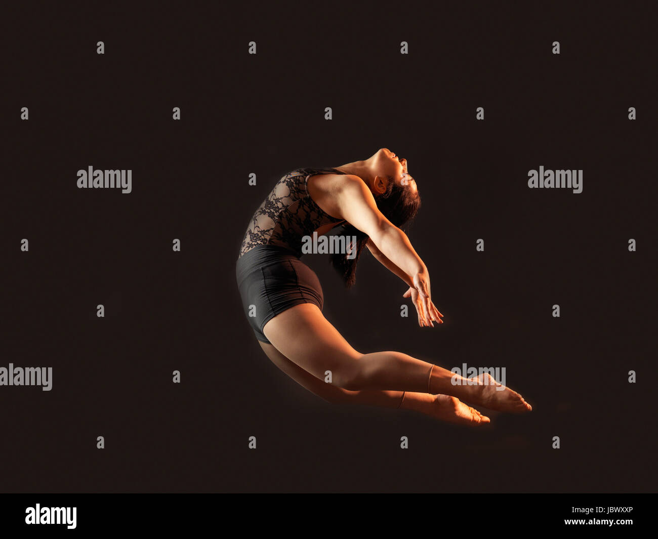 Low key shot of young female dancer bending backwards whilst leaping ...