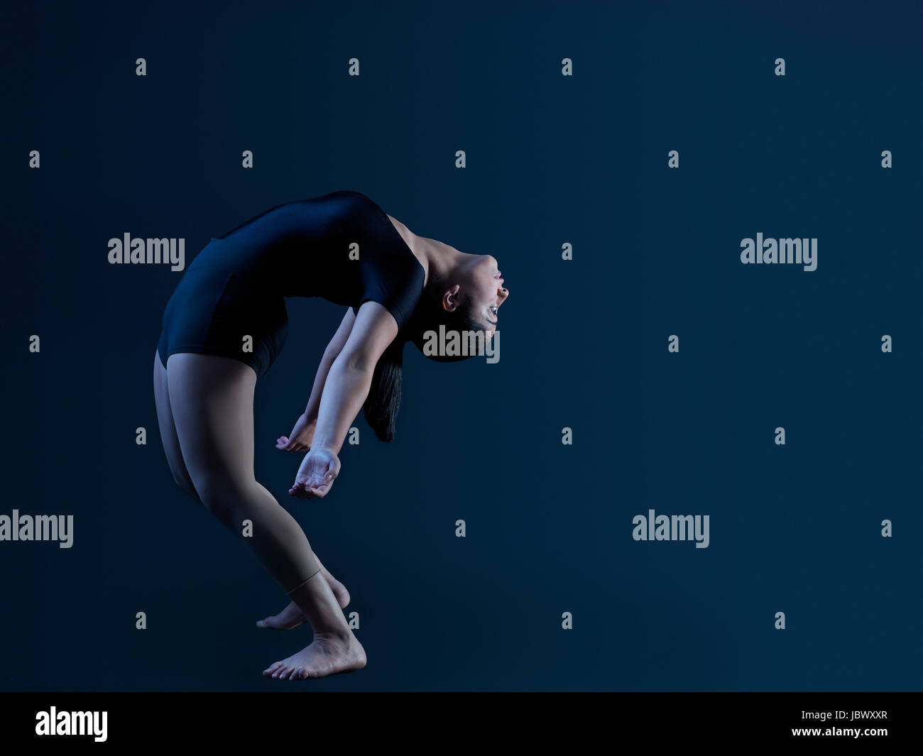 Low key shot of young female dancer standing and bending over backwards ...