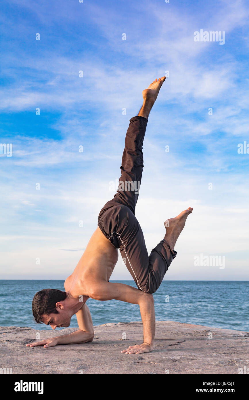 Young man outdoors, in yoga position, balancing on hand and forearm ...
