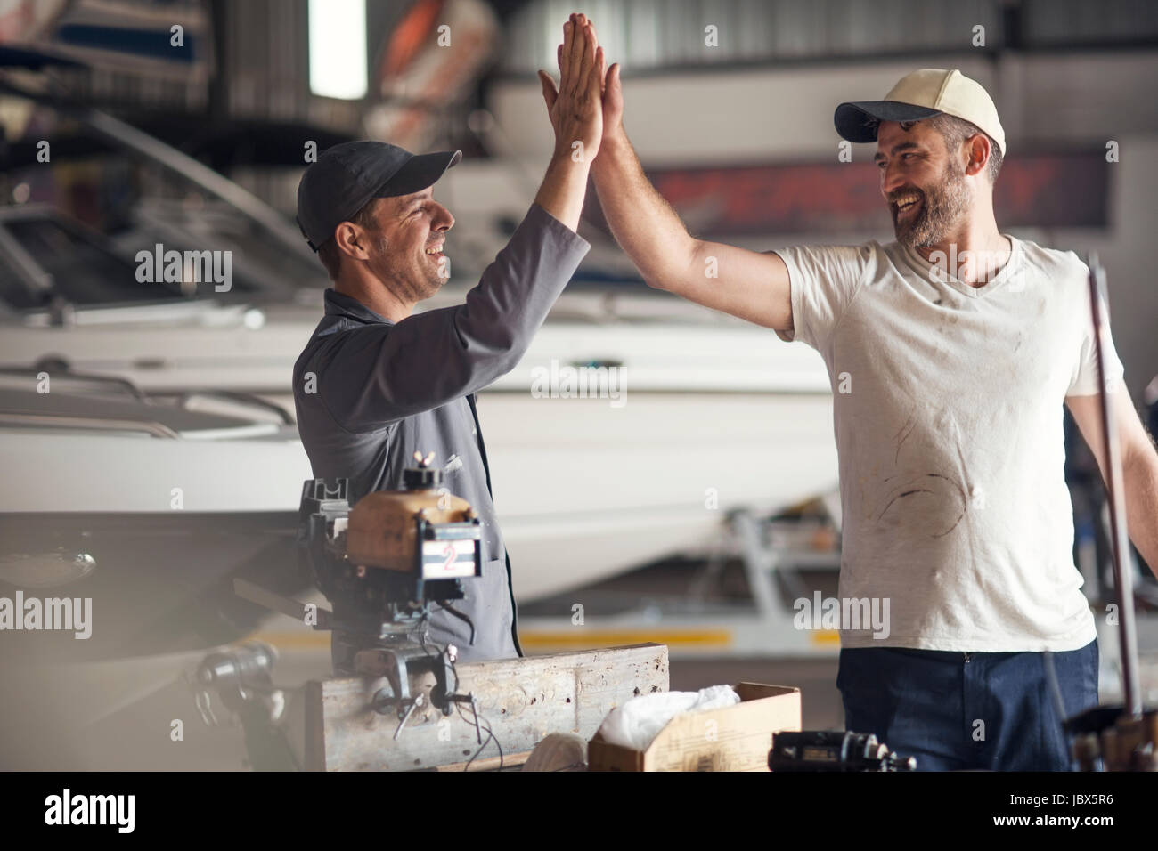 Two men high fiving in boat repair workshop Stock Photo - Alamy