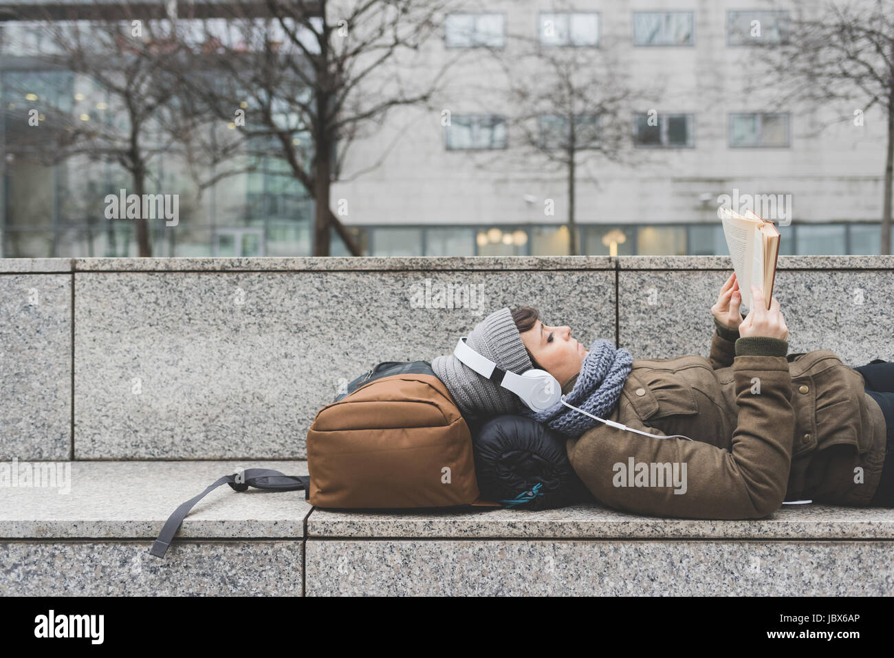 Female backpacker lying on back reading book on wall Stock Photo - Alamy