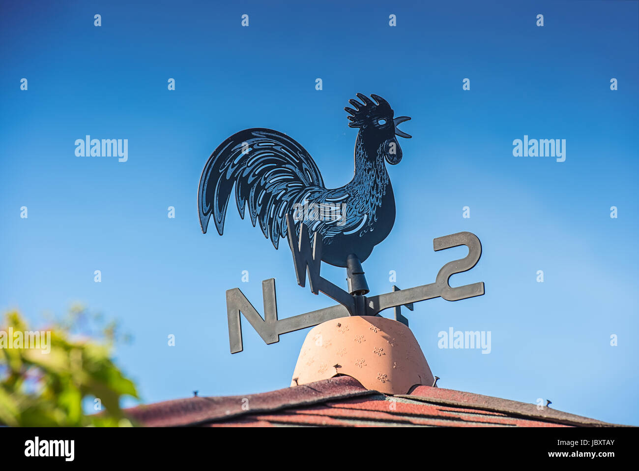 Black and blue metal weathercock on roof with blue sky unfocused ...