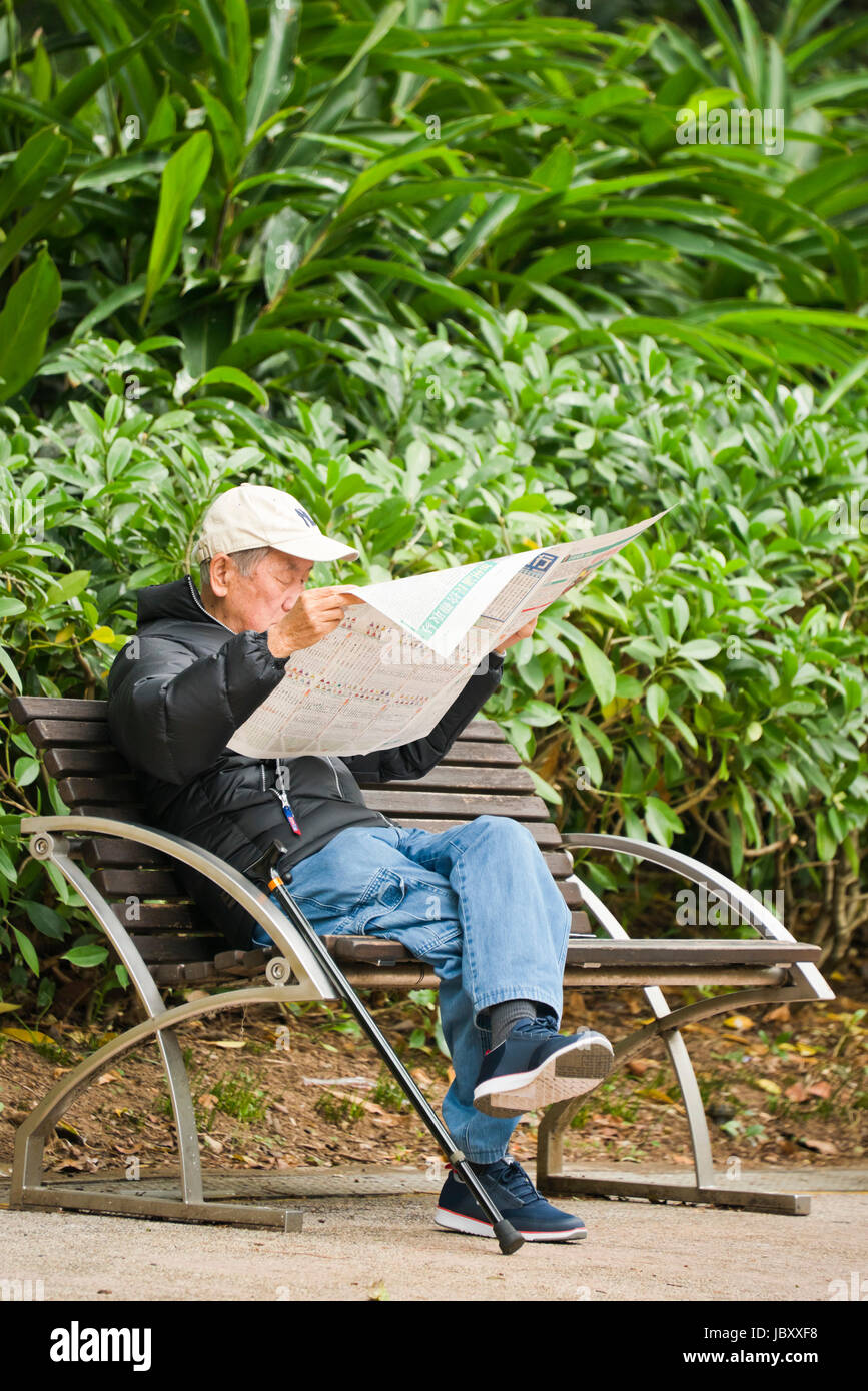 Vertical portrait of an old man reading the racing pages in Hong Kong ...