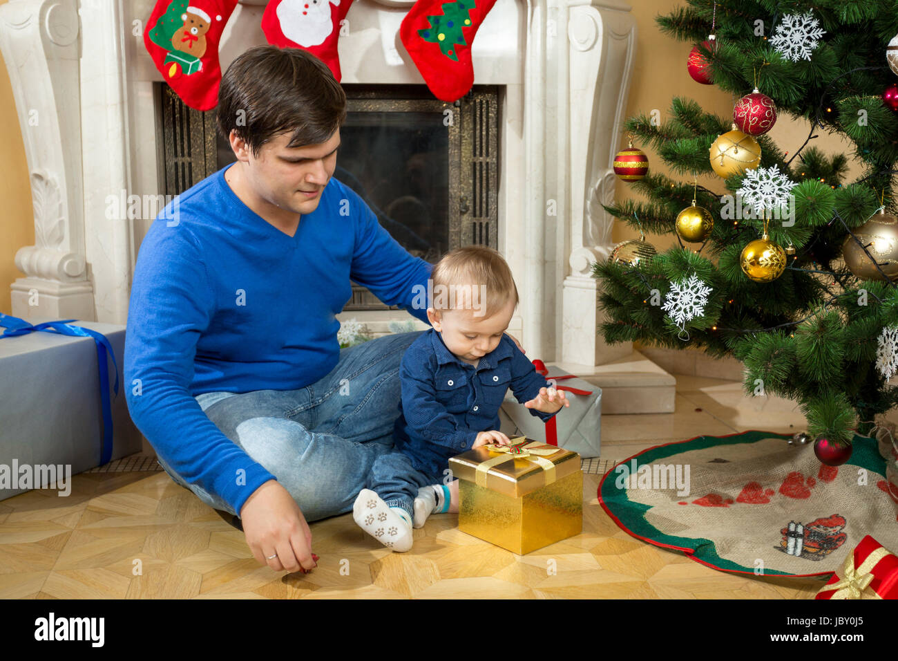 Cute baby boy with his father opening Christmas gifts on floor at ...
