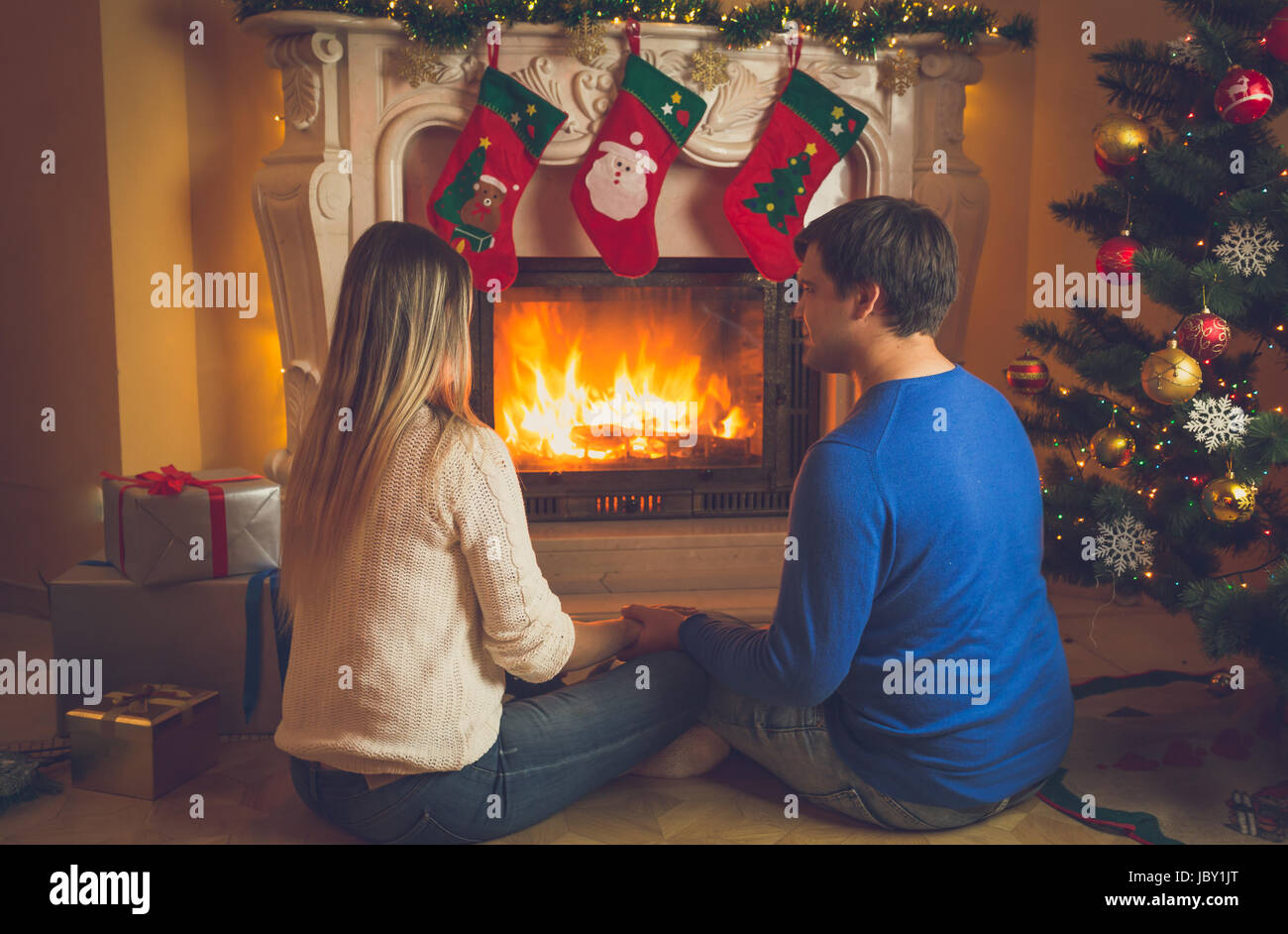 Toned image of young couple in love sitting by the fireplace decorated ...