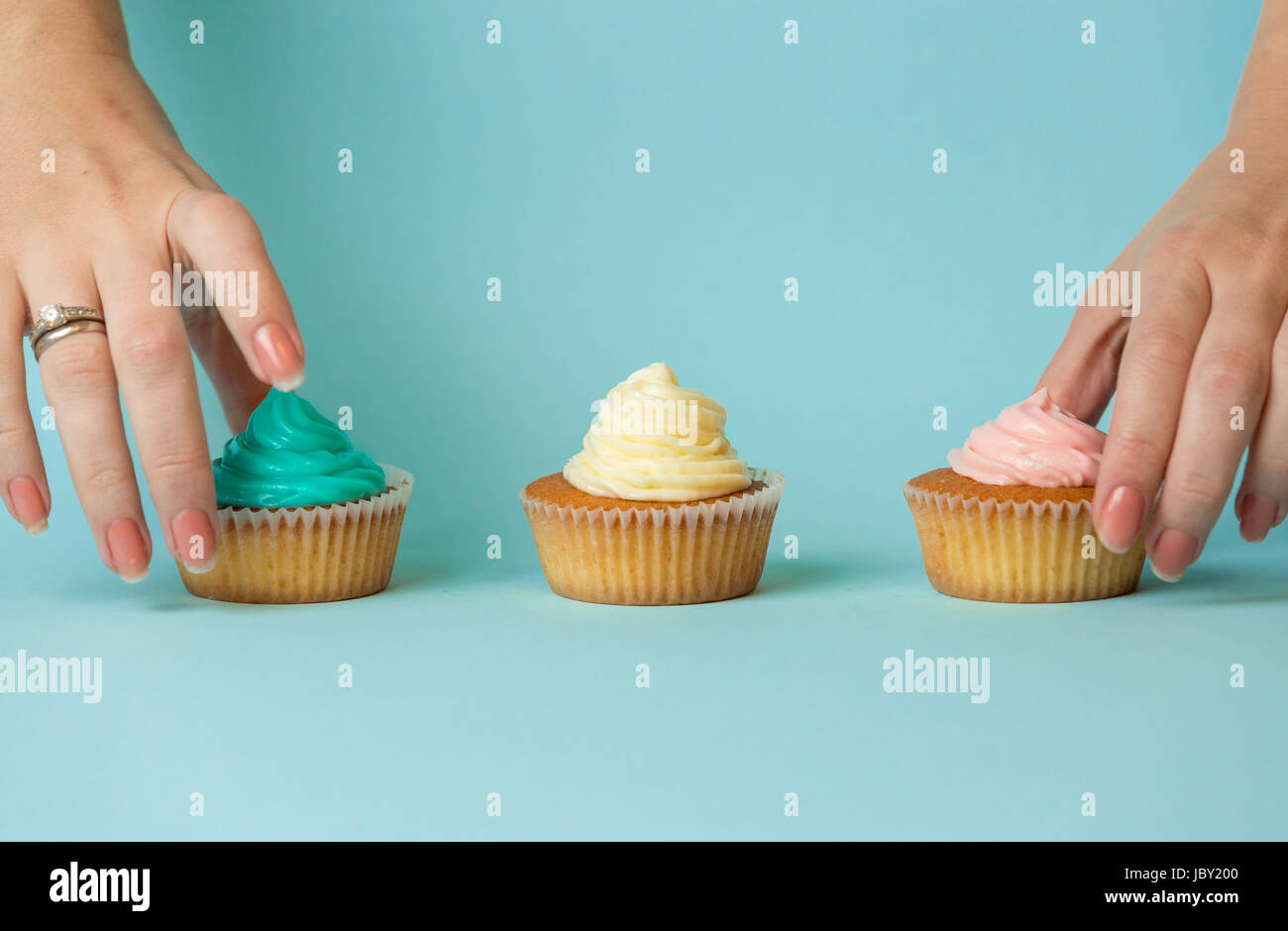 Closeup photo of female hands choosing between three colorful cupcakes ...