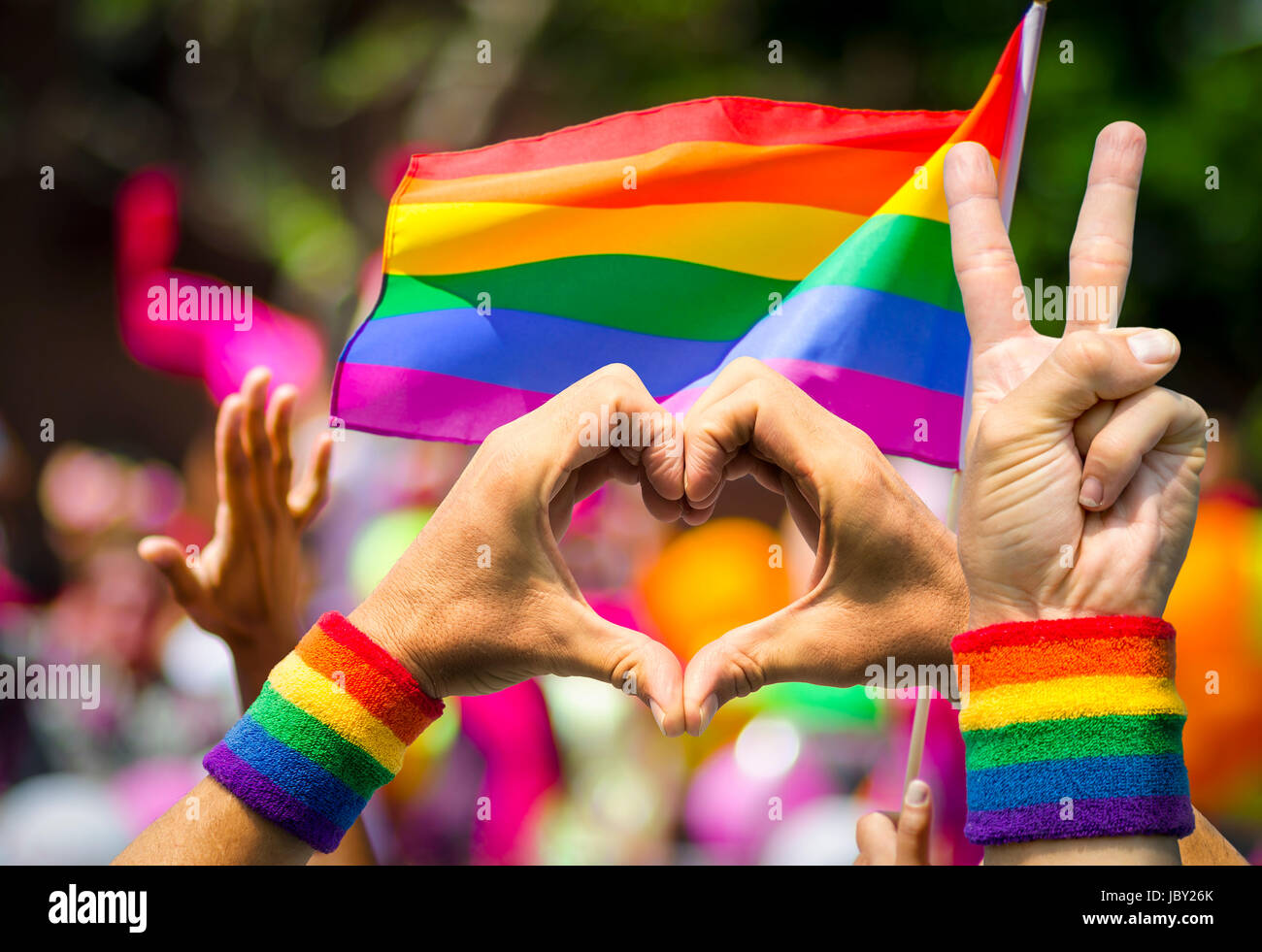 Supporting hands make peace and heart signs in front of a rainbow flag ...
