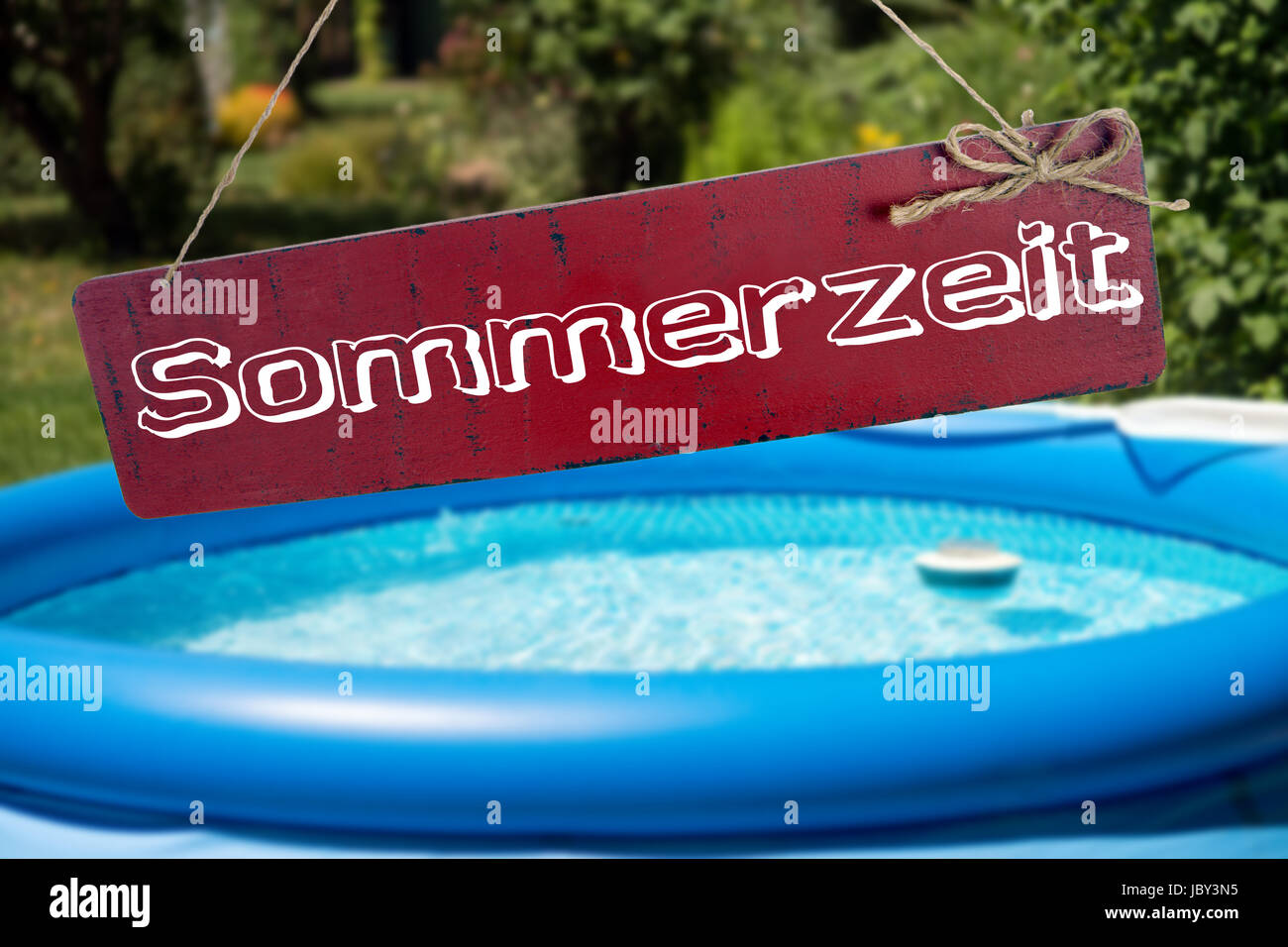 Swimming pool in a garden and sign with the german word Summer time ...