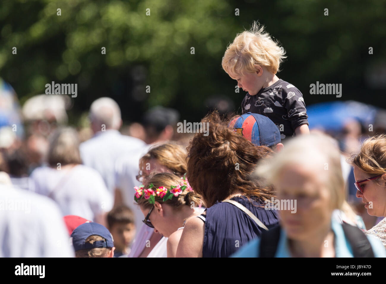 Young blond haired child (boy) sat on fathers shoulders in crowd at Ham ...