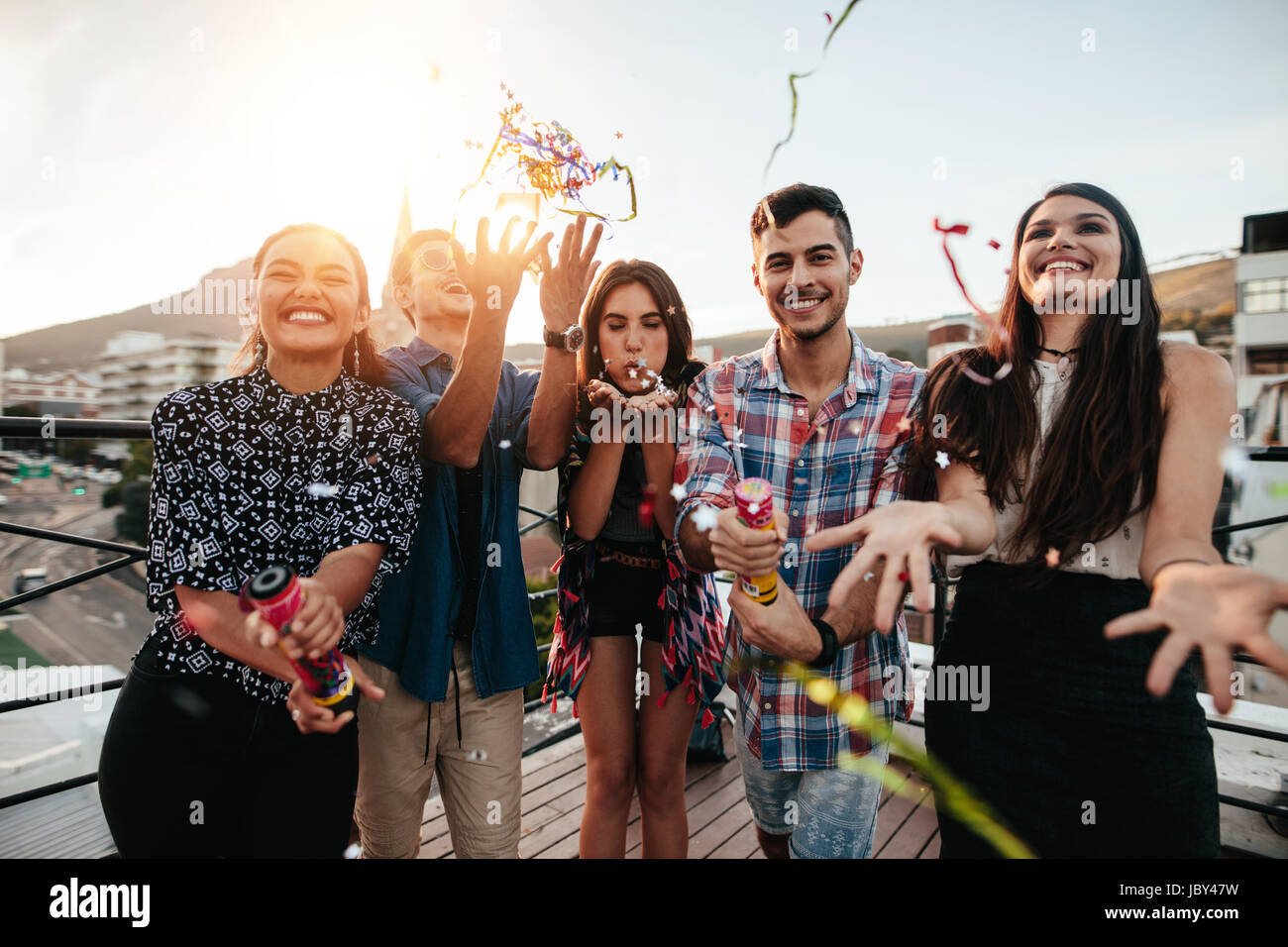 Group of happy young people throwing confetti while enjoying rooftop ...
