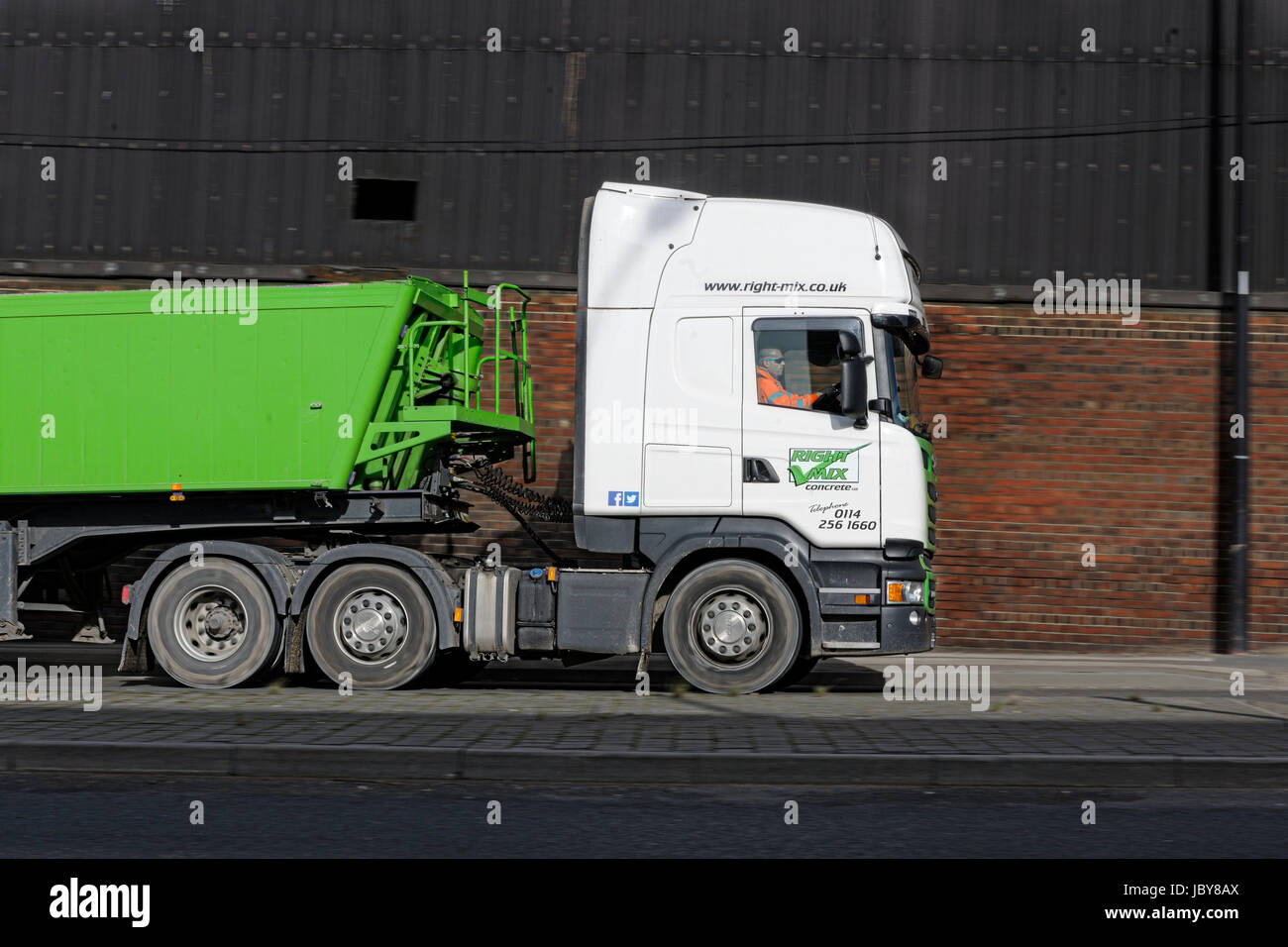 Scania bulk tipper driving along a city street in an industrial area of ...