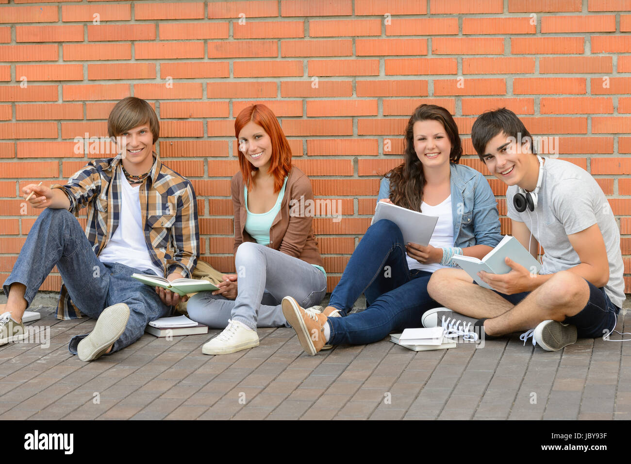 College students with books sitting ground by brick wall Stock Photo ...