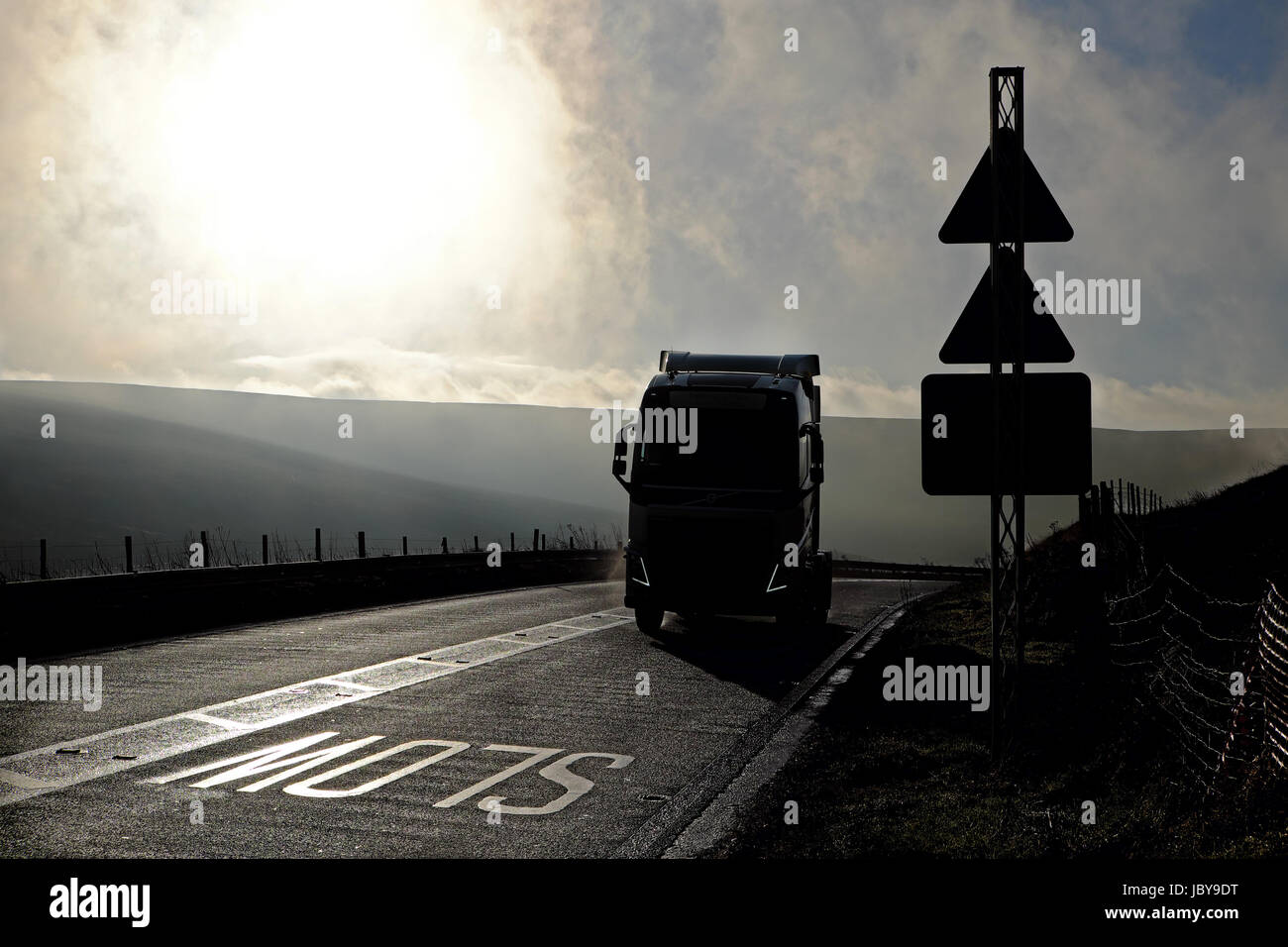 A Volvo tractor unit silhouetted by the sun rounds a bend on the ...