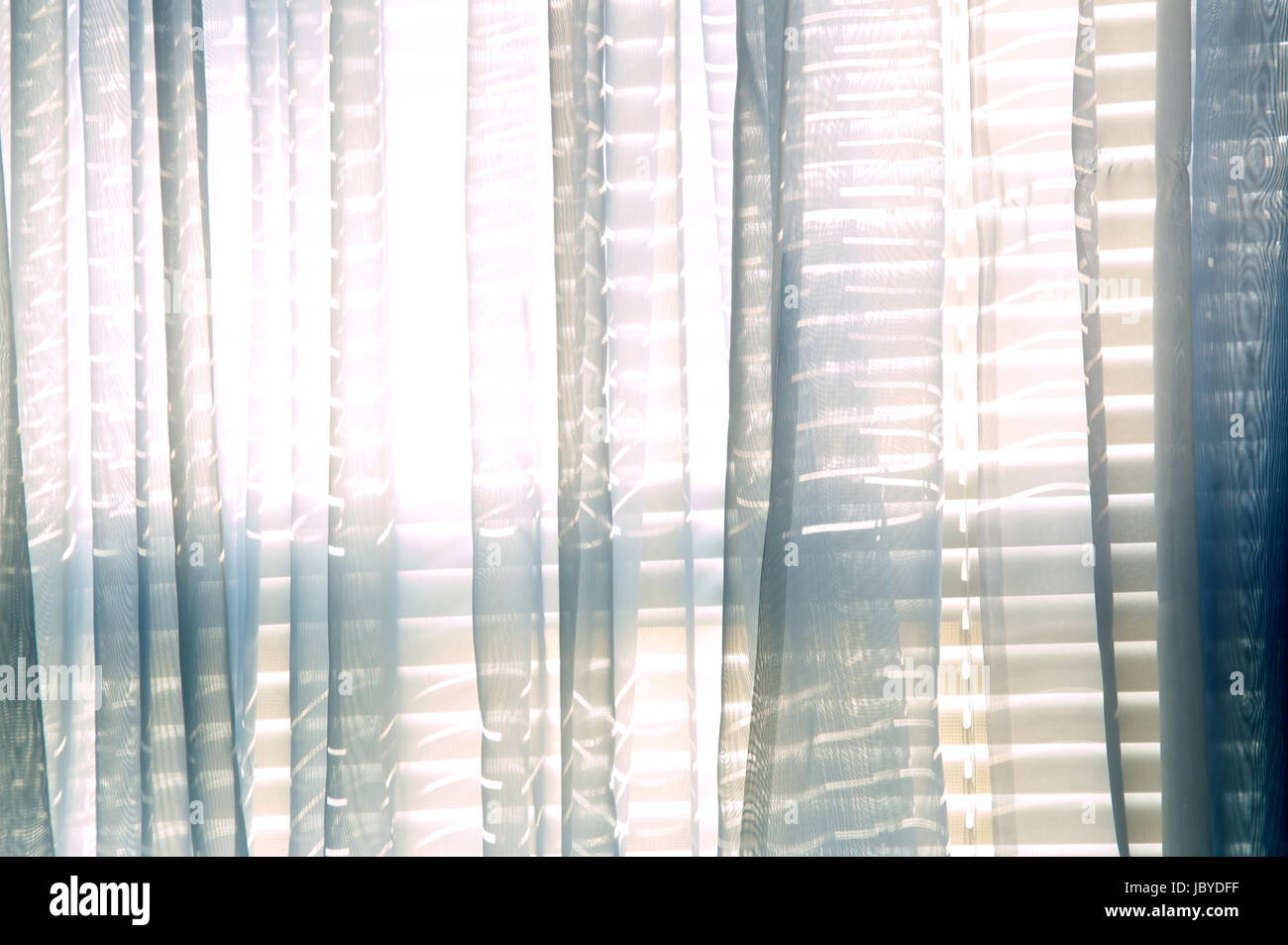 Bright daylight shines through a window draped with blue sheer curtains ...