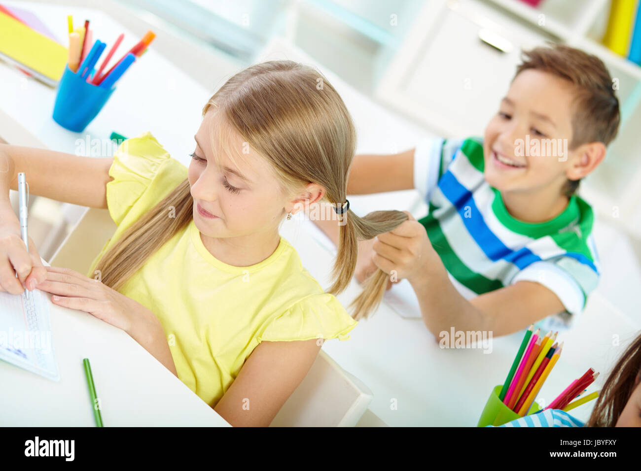 Portrait of lovely schoolgirl drawing at workplace while her schoolmate ...
