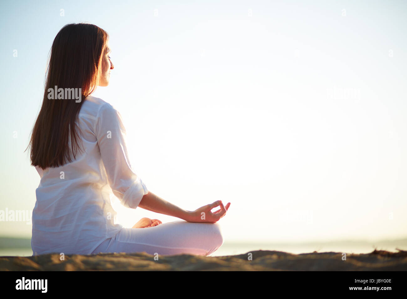 Side view of meditating woman sitting in pose of lotus against clear ...
