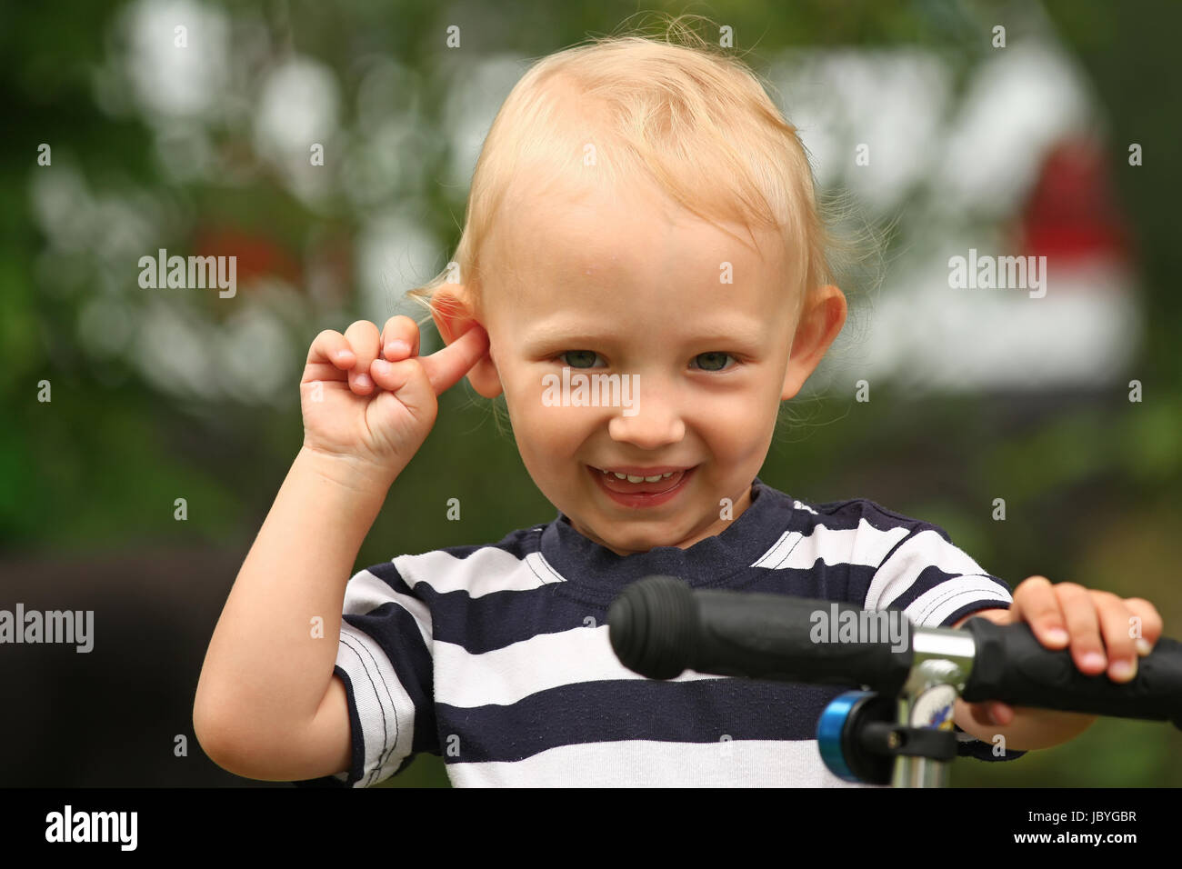 Smiling blond boy in the striped shirt on a scooter is sticking finger ...